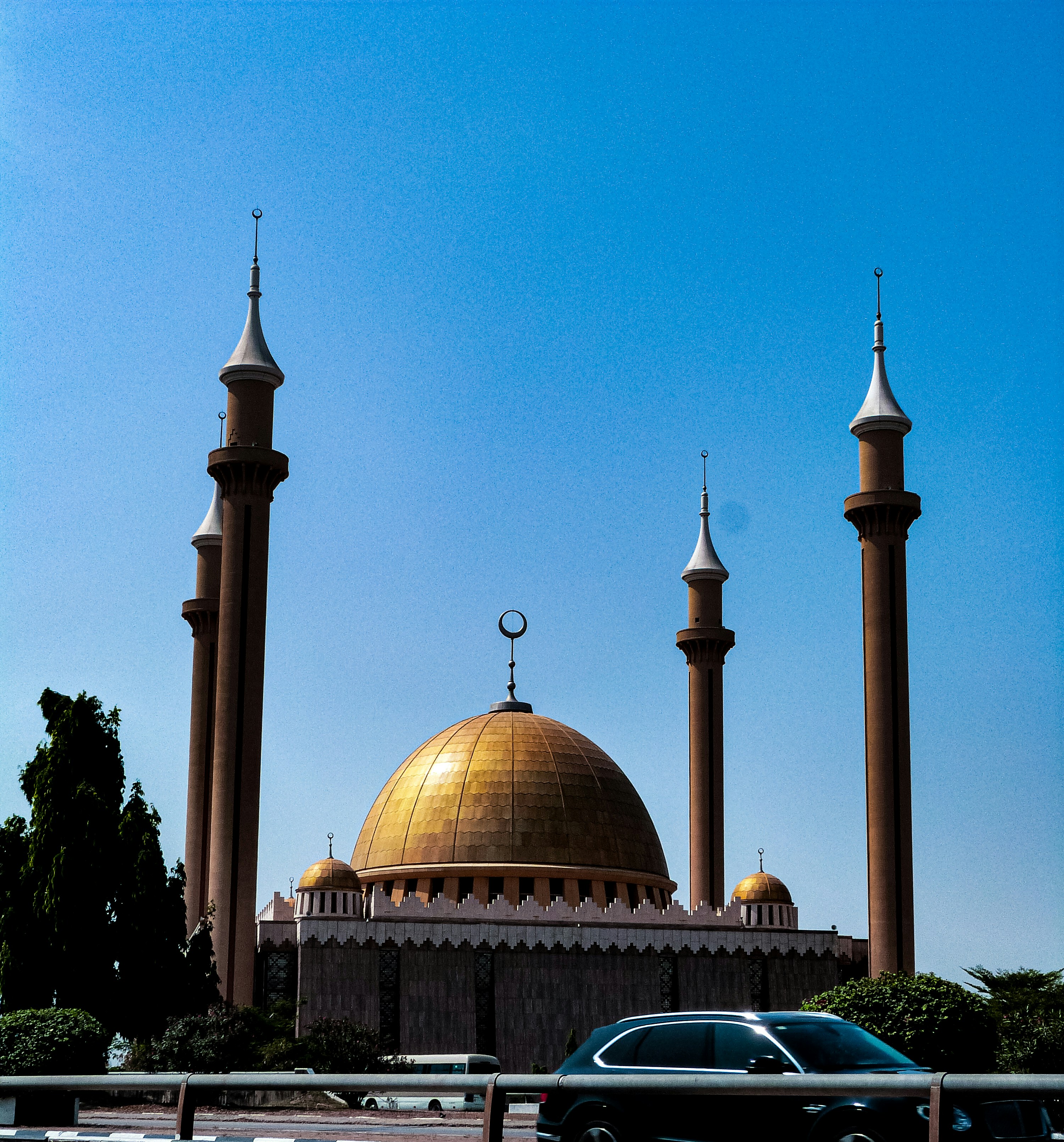 Golden-domed mosque with four minarets against a clear blue sky, car in the foreground.