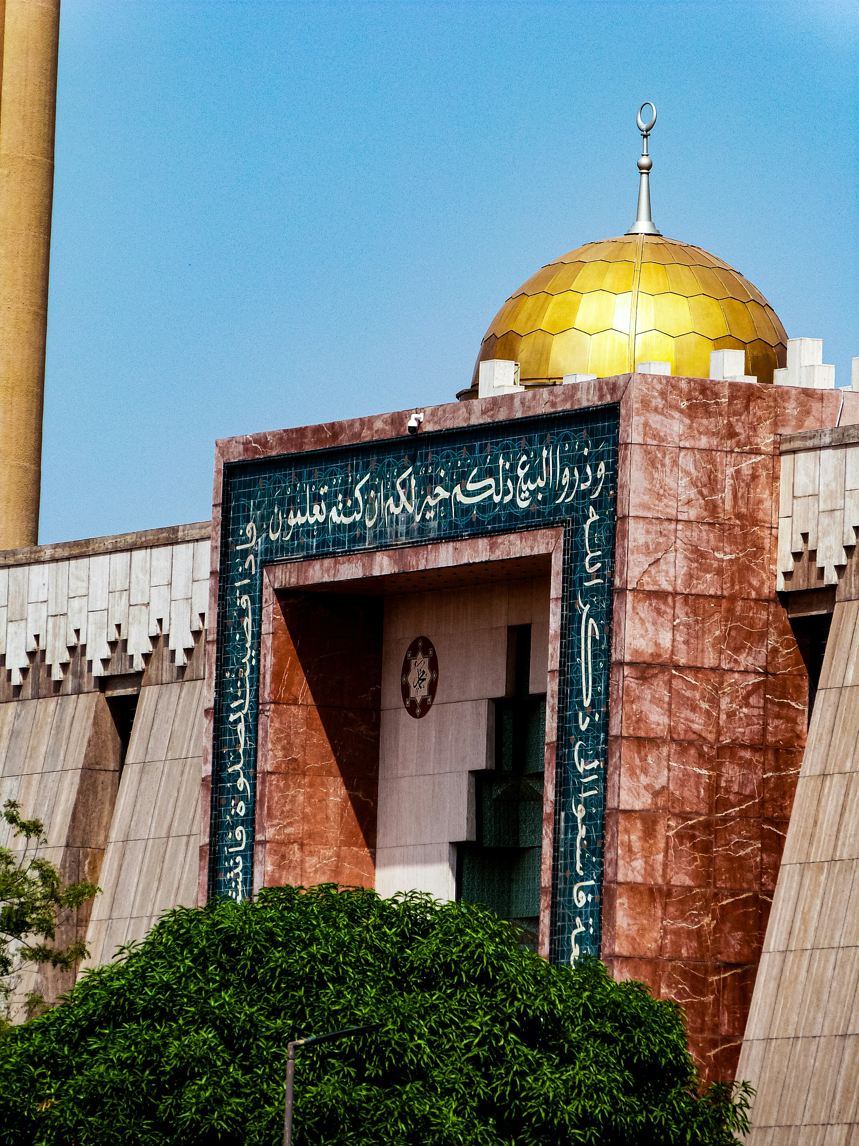 Golden dome atop a mosque entrance framed by intricate calligraphy, set against a clear blue sky.