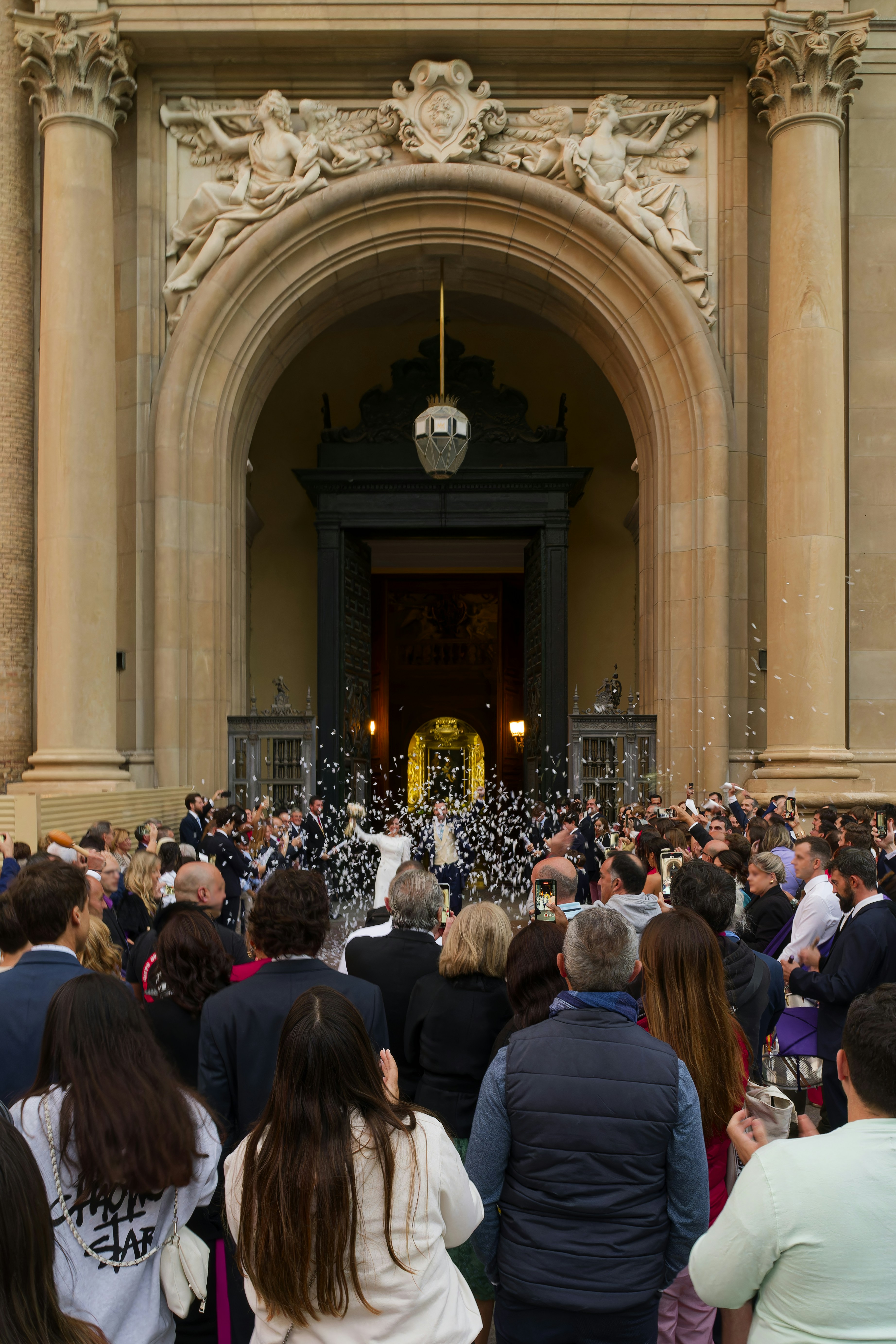 Newlyweds exit the Cathedral-Basilica of Our Lady of the Pillar, surrounded by celebrating guests and flying confetti.