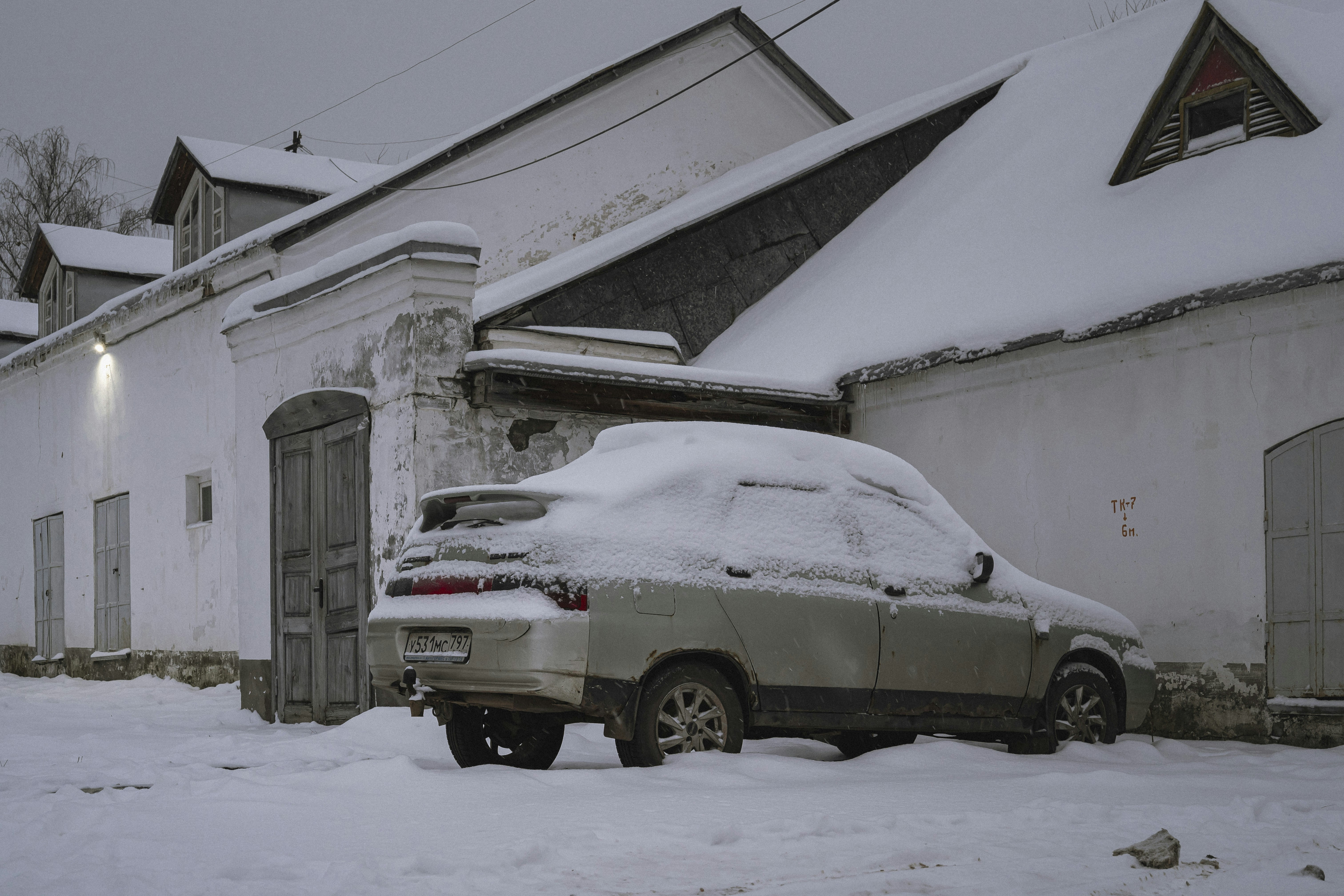 Snowbound Sedan Beneath a Weathered Roofscape