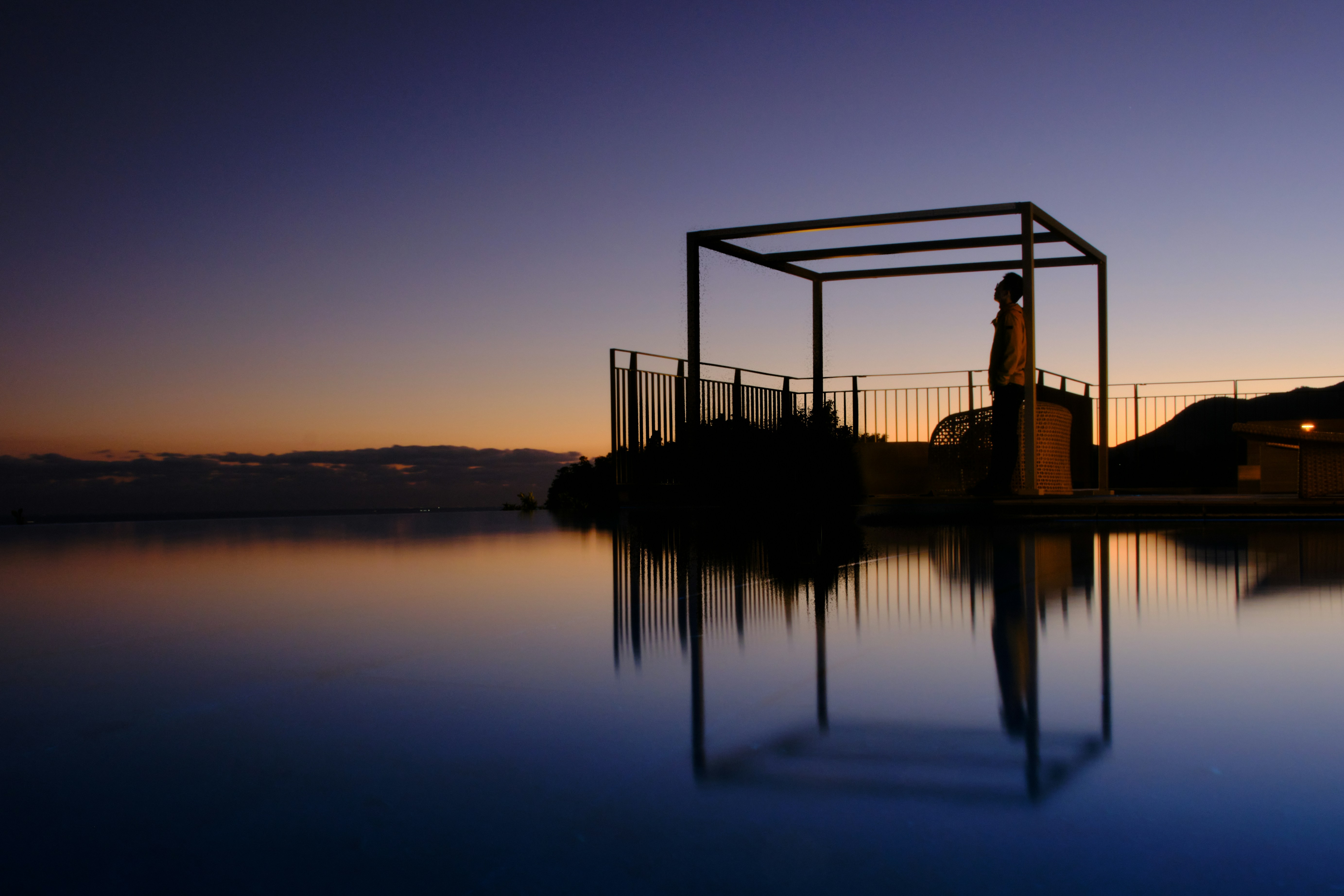 Silhouette by the Water: A Lone Figure under the Modern Pavilion