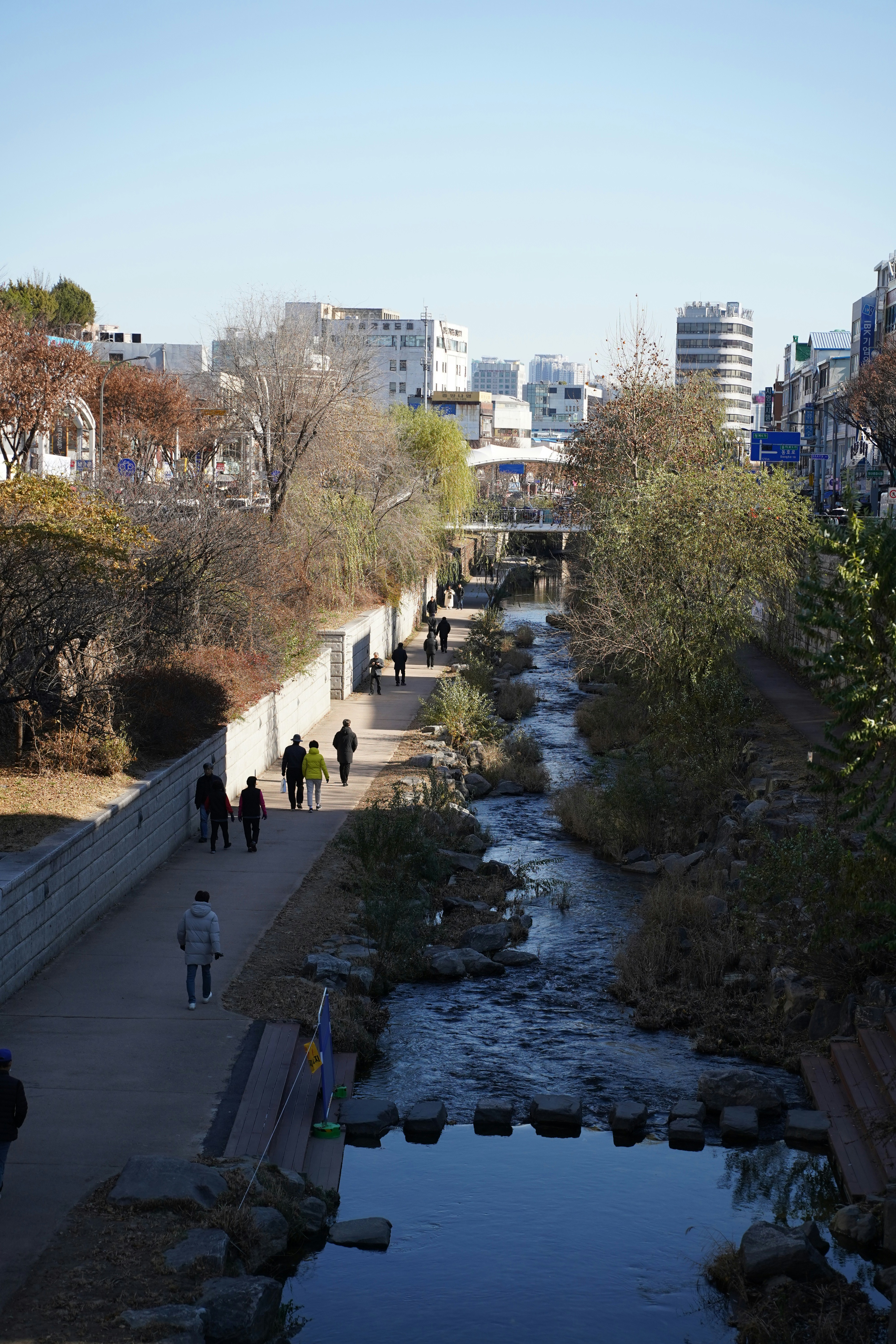 Riverwalk in Light: Pedestrians tracing a tranquil urban canal beneath a clear sky