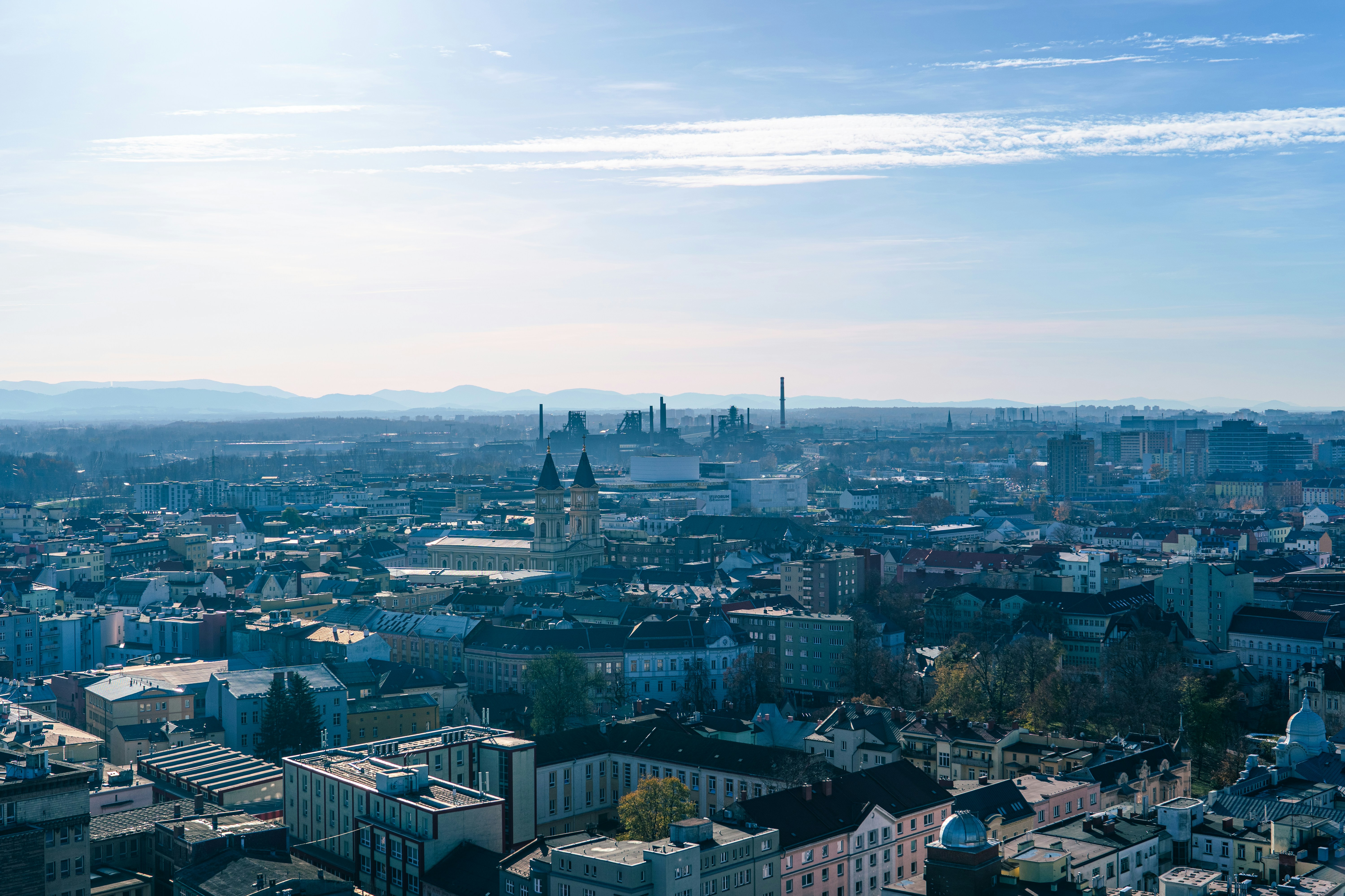 A sweeping aerial view of a cityscape featuring a blend of historical architecture and industrial structures under a clear blue sky.