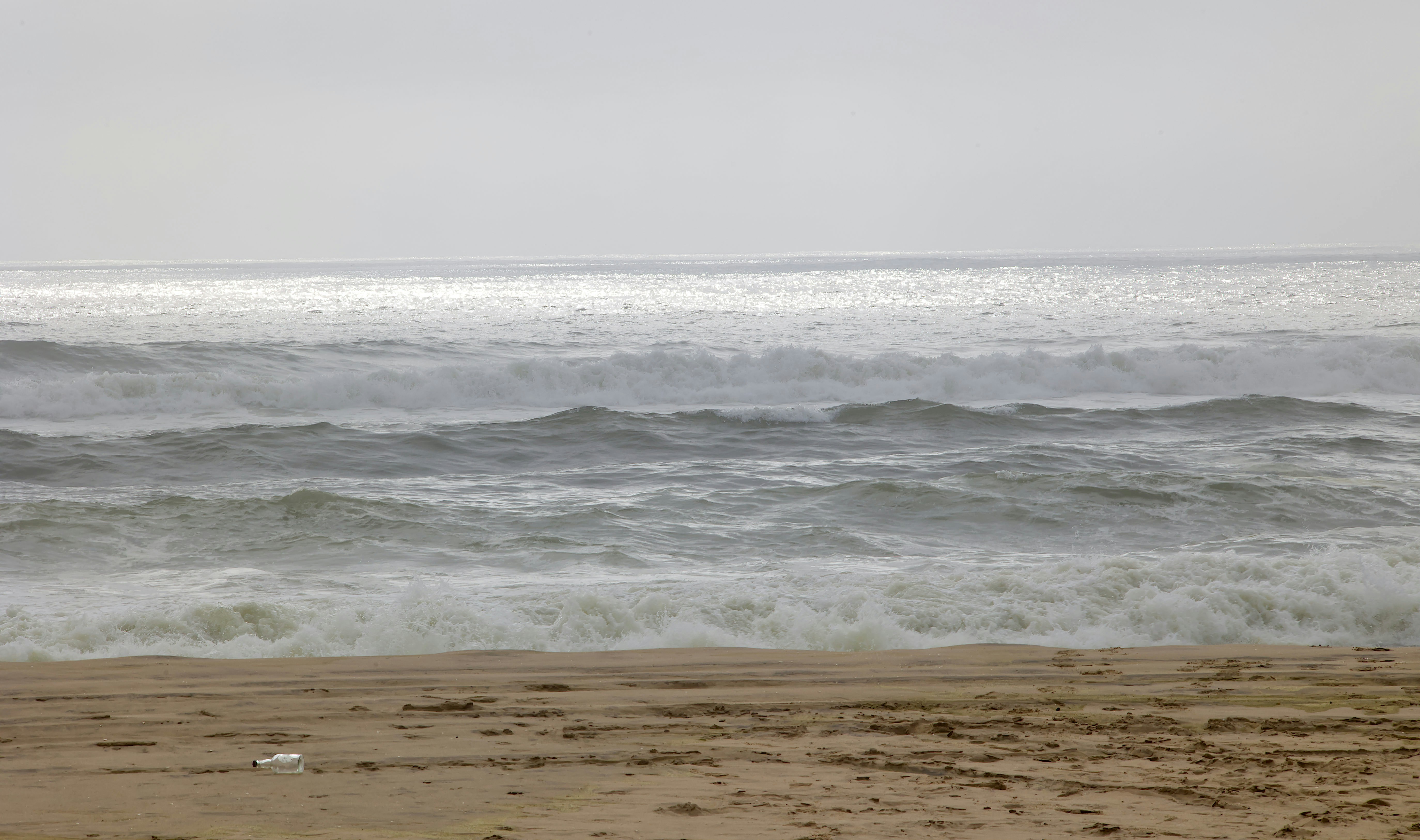 Gentle waves roll onto a sandy beach under an overcast sky.