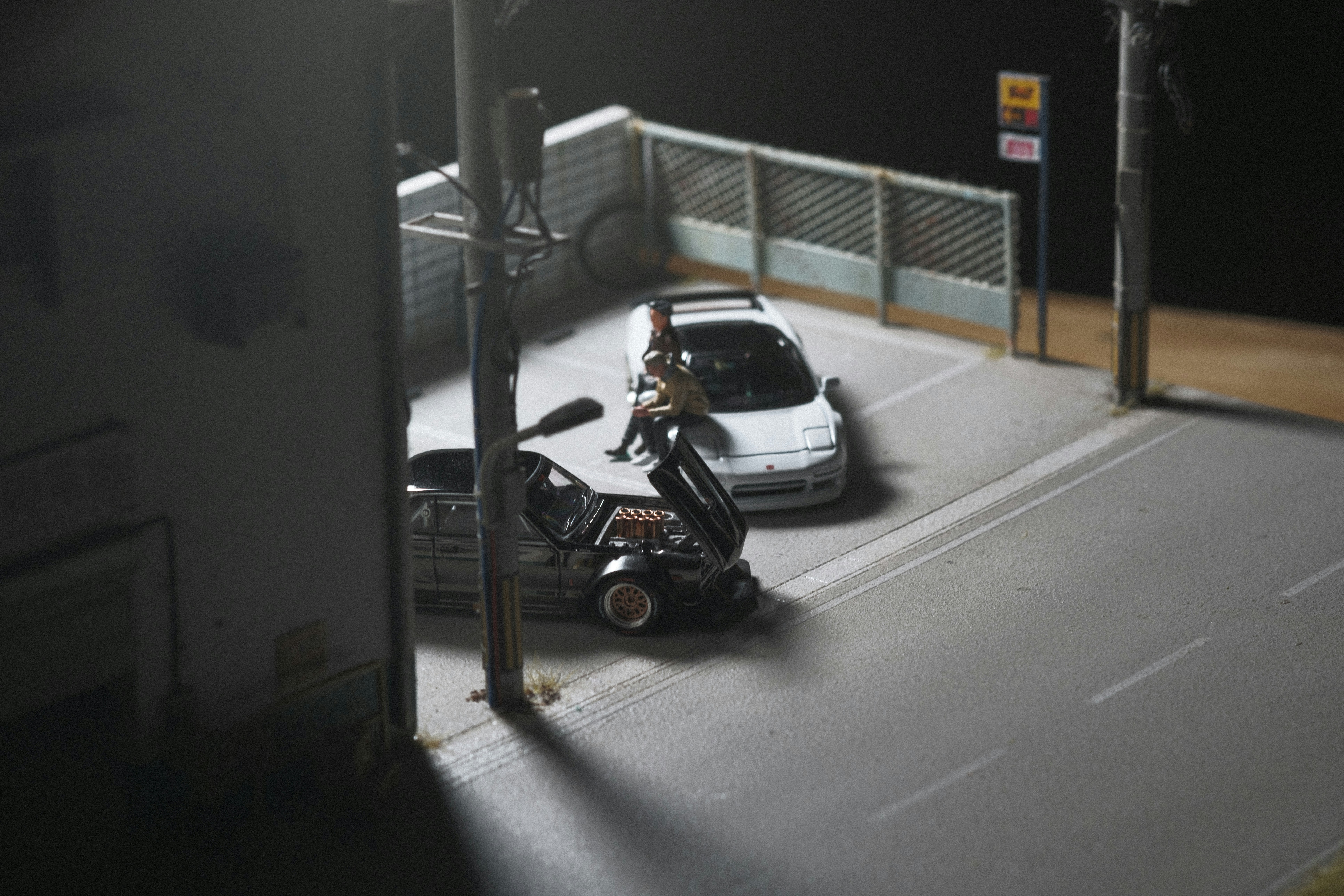 Two miniature figures and cars in a detailed diorama of a street parking area.