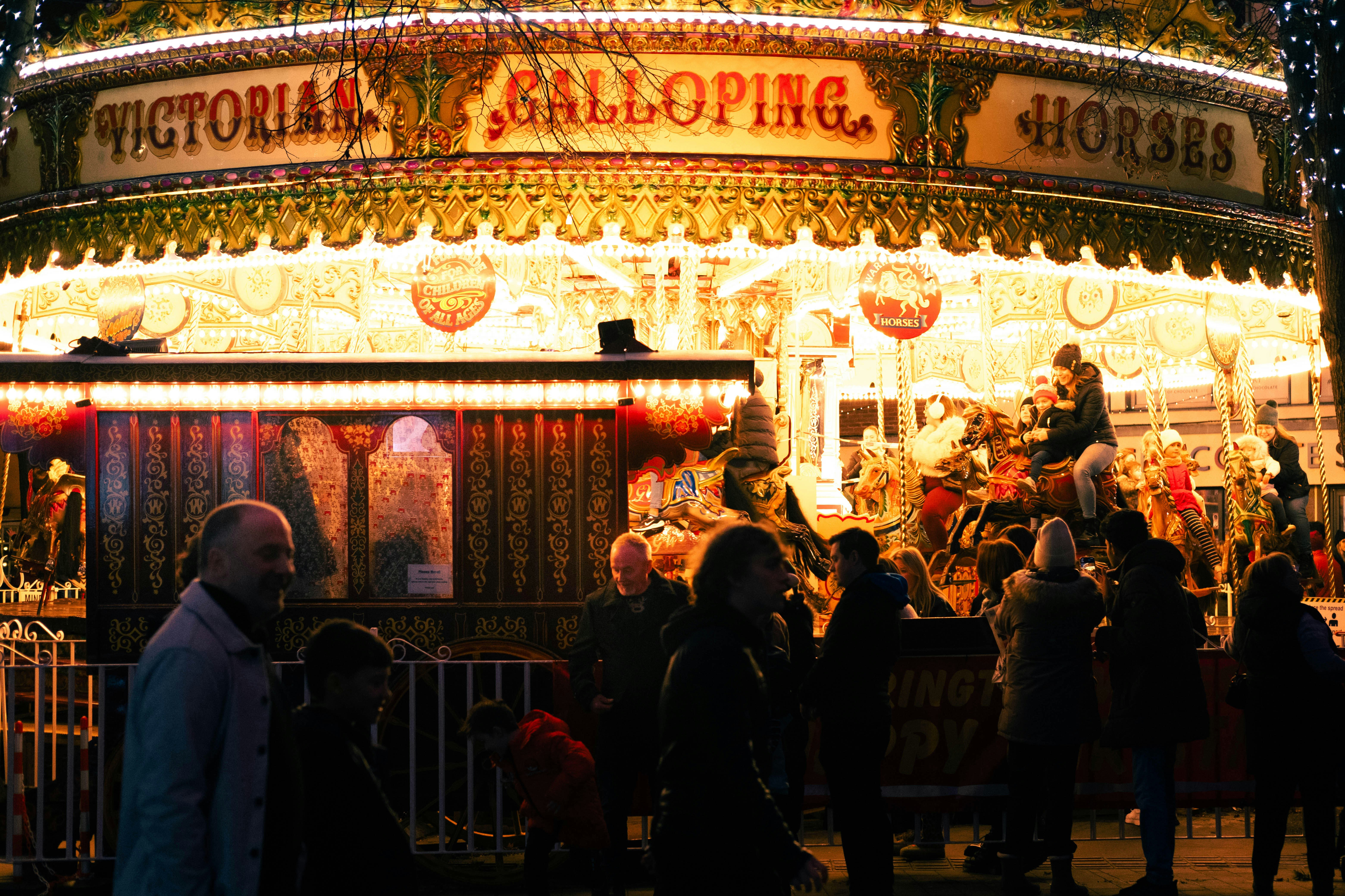 A group of people standing around a merry go round photo – Free ...