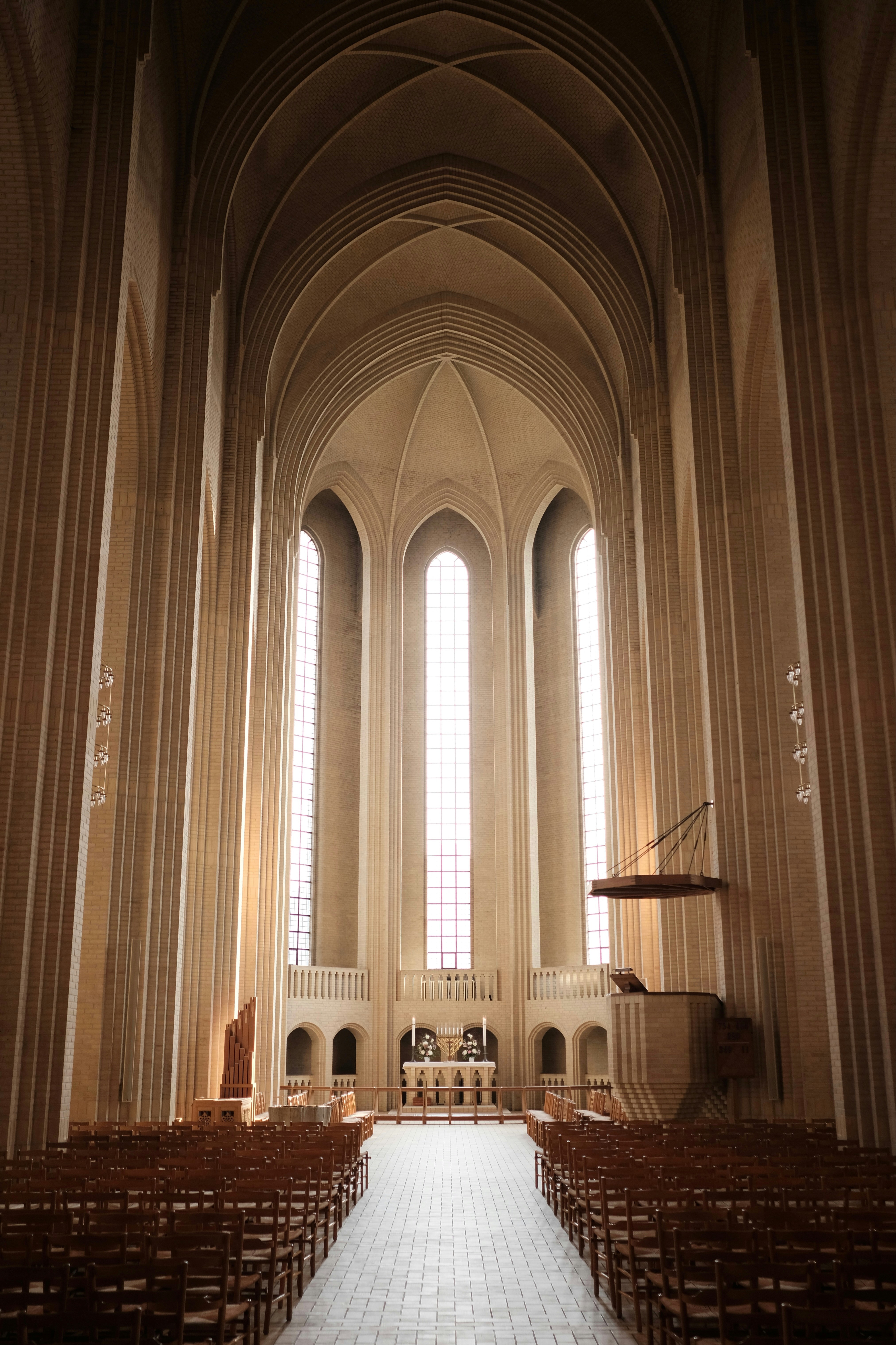 Soaring arches and columns in a cathedral interior with soft light filtering through tall windows.