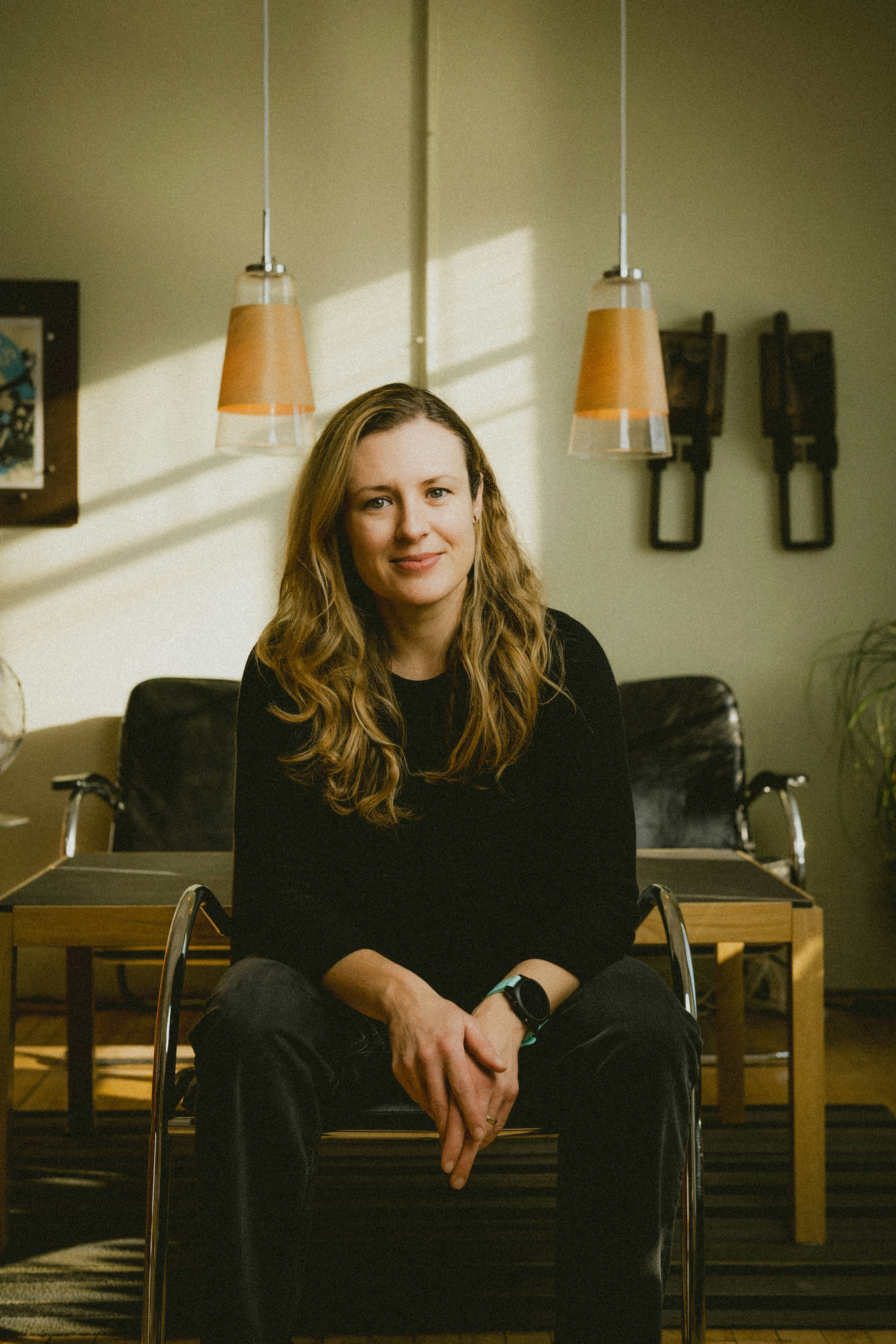 Woman seated in a modern living room, bathed in warm natural light with soft shadows and earthy tones.