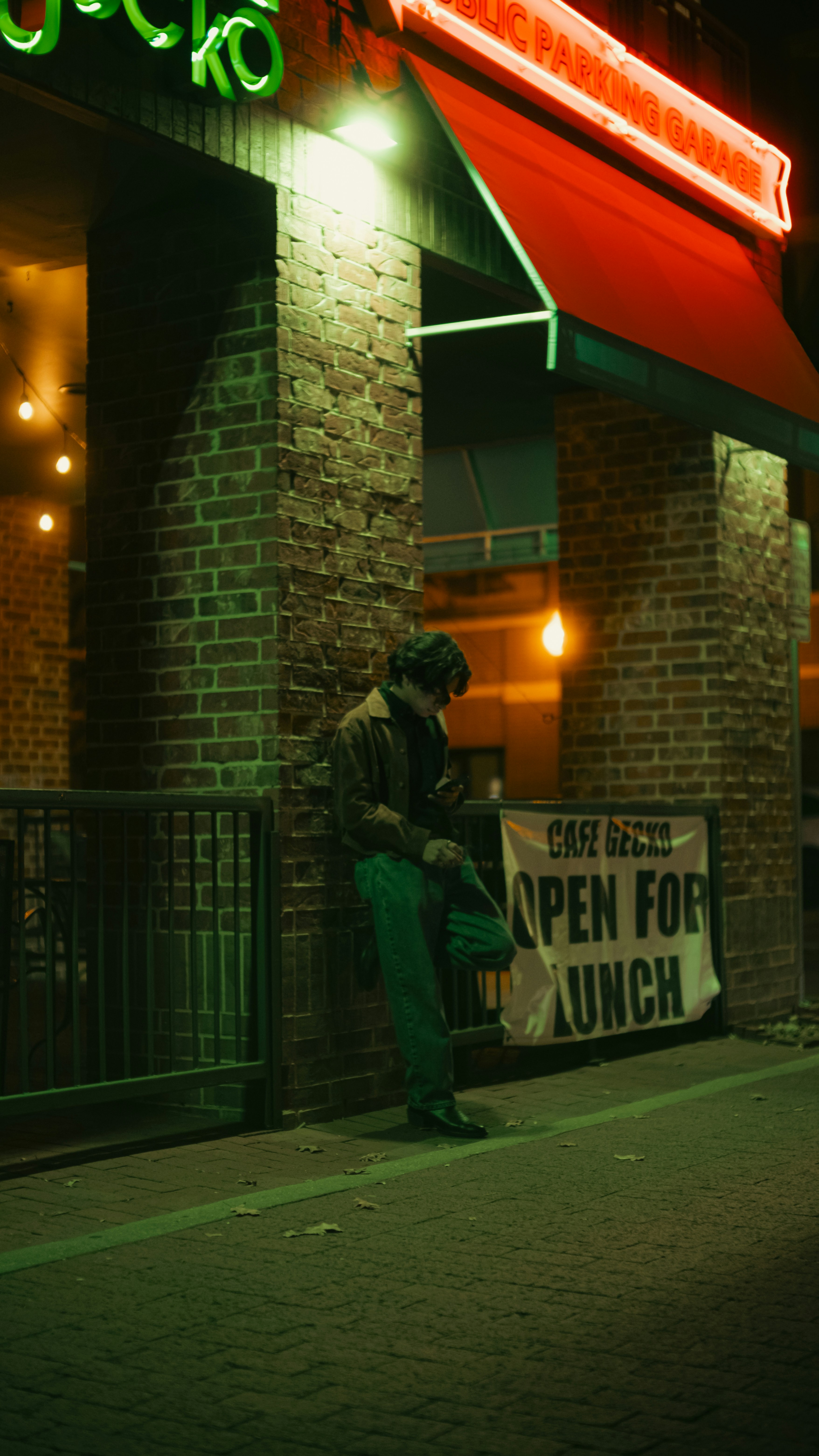 Person leaning against a brick wall under neon lights at night.