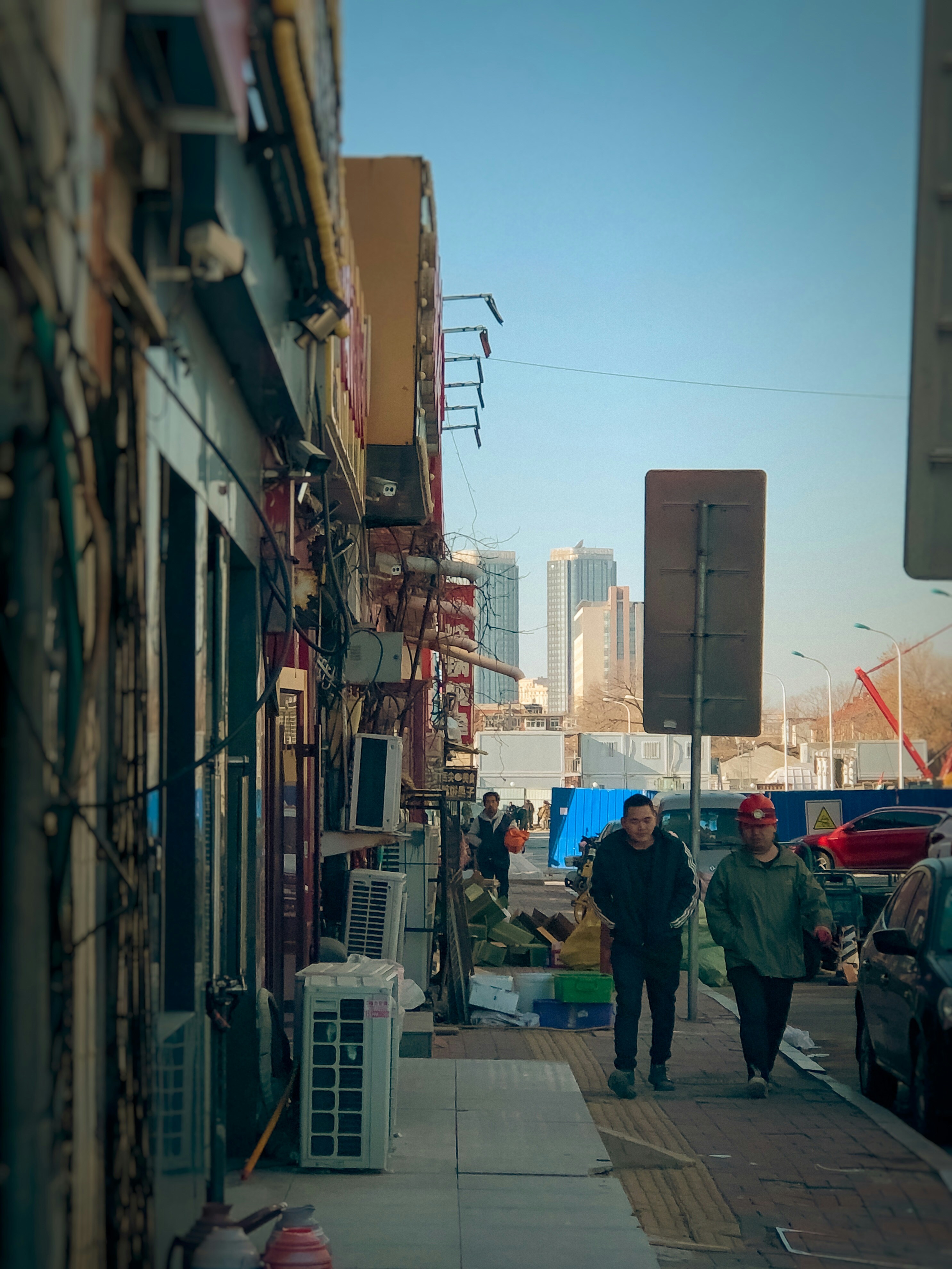 Two Walkers in a Narrow City Street: Cluttered Facades and Distant Towers