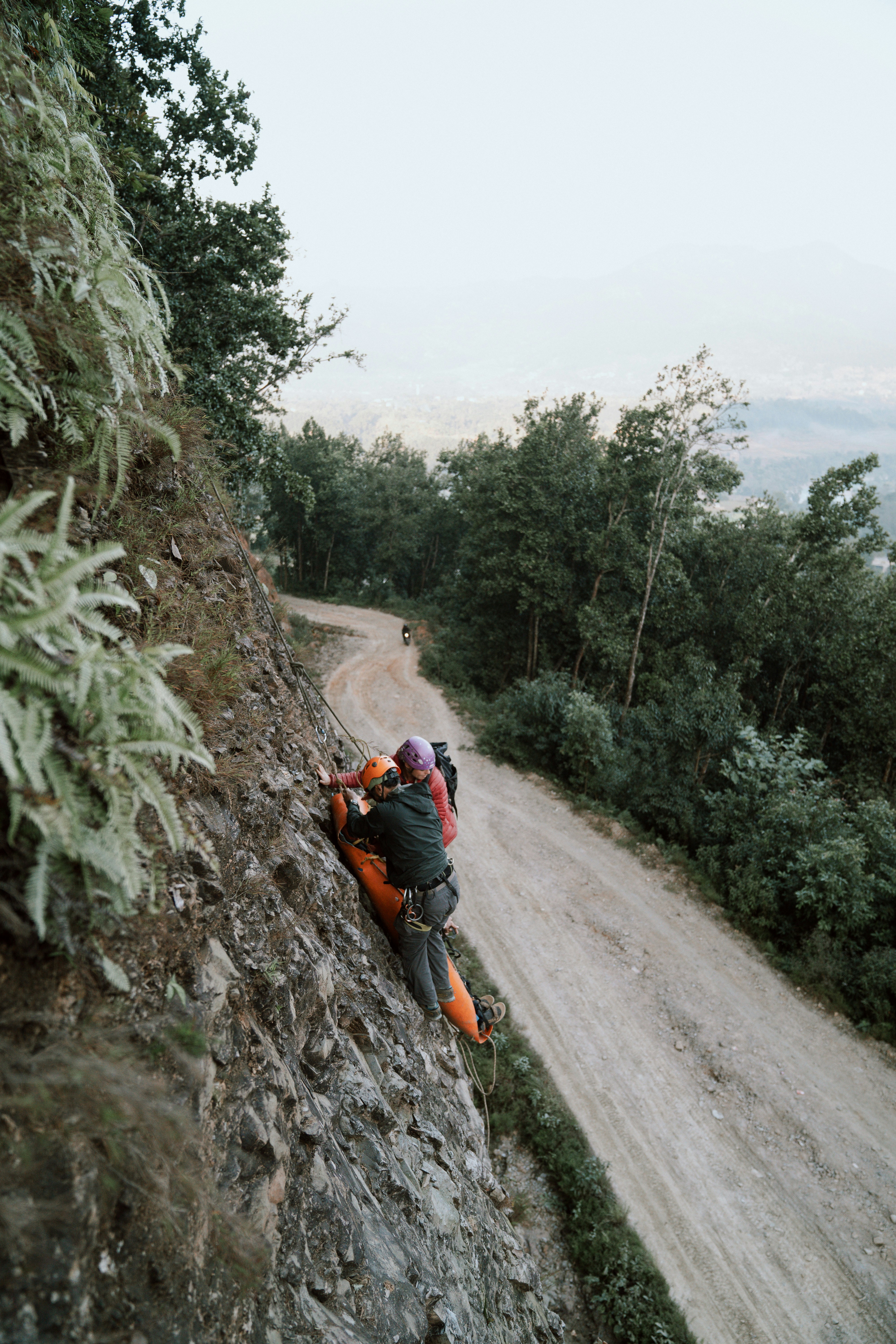 Cliffside Climb: Climbers Grapple Up a Narrow Rock Face Above a Winding Road