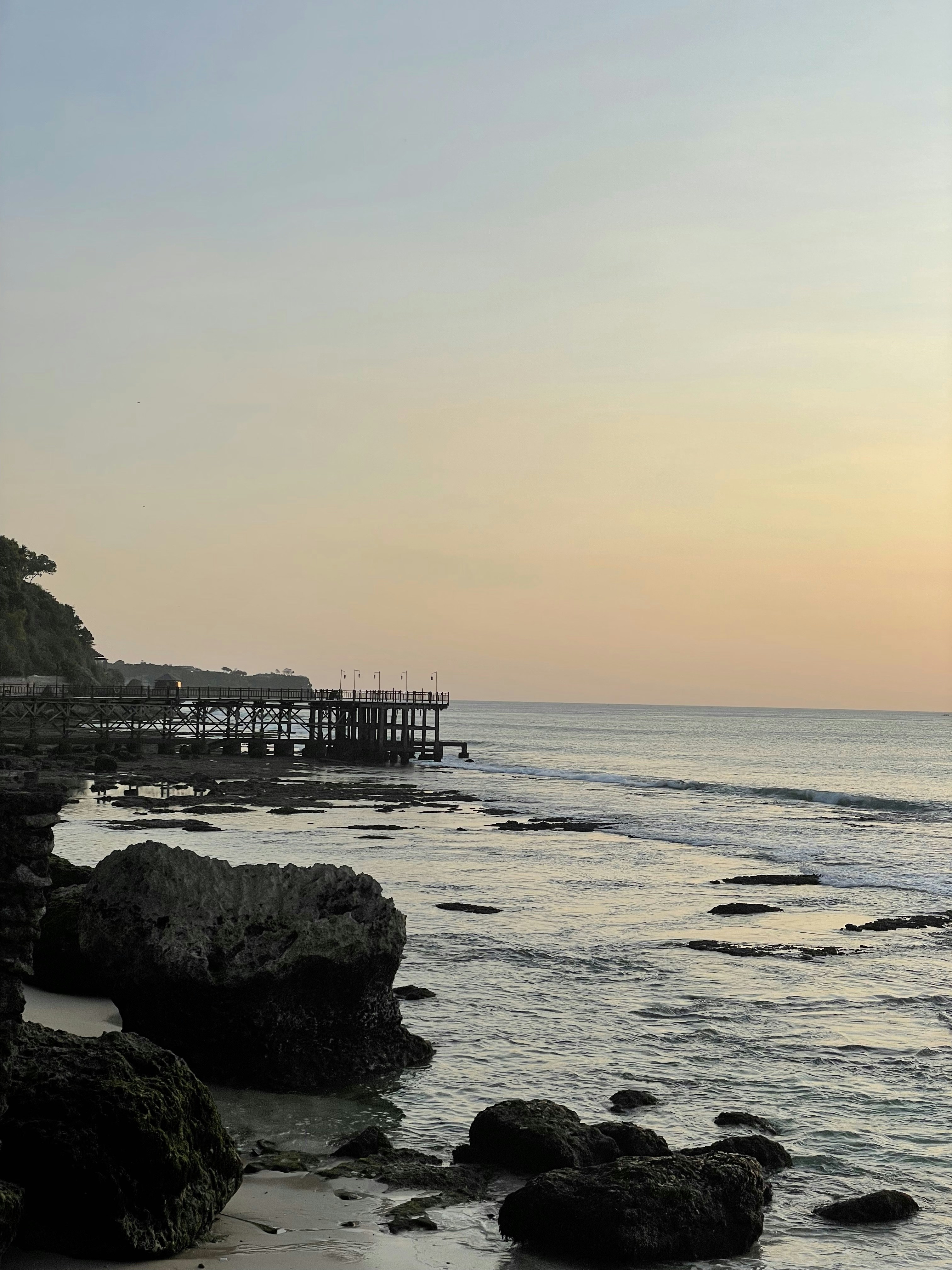 The sun is setting over the ocean with a pier in the distance photo ...