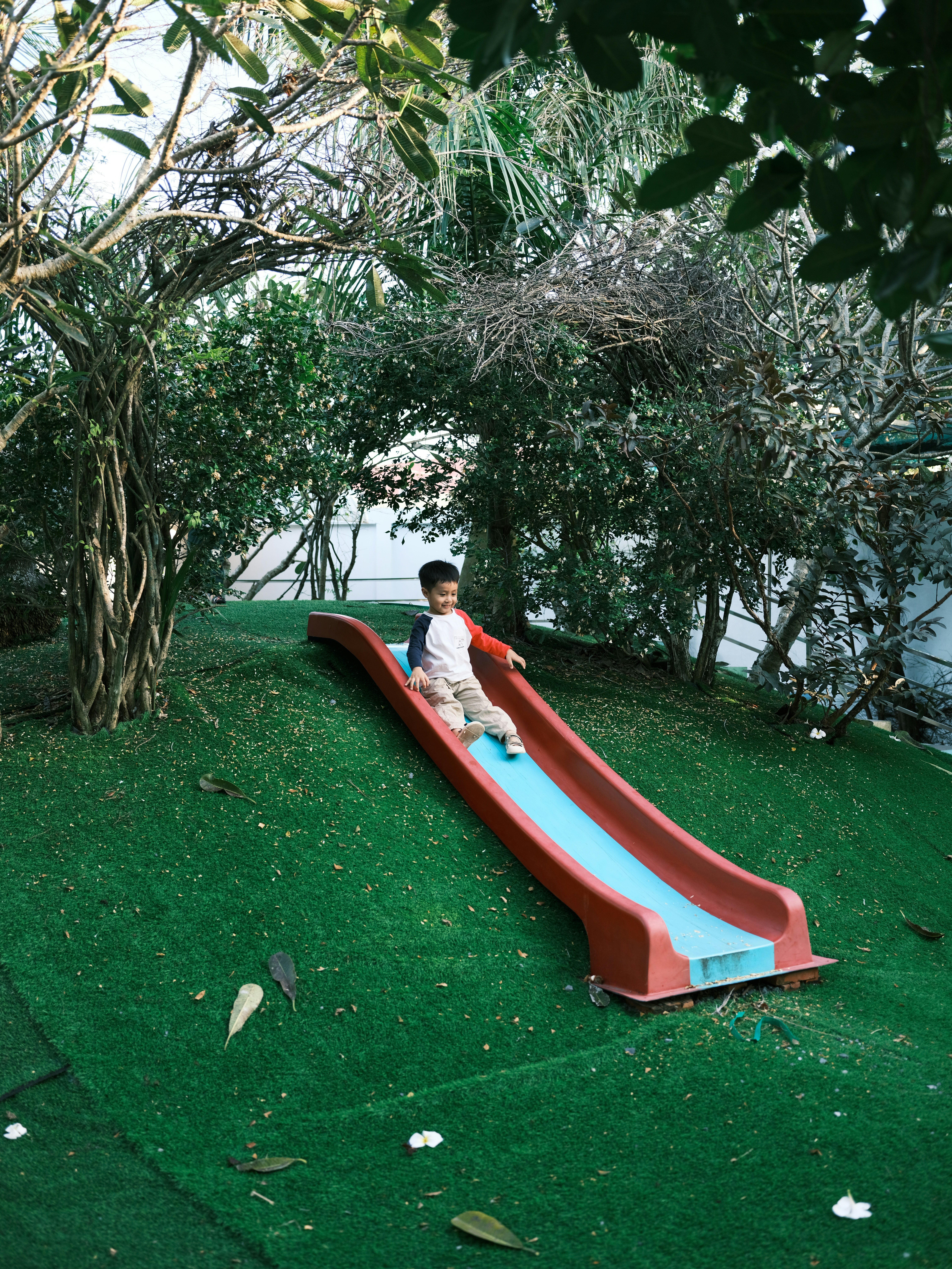Child sliding down a red slide surrounded by lush greenery.