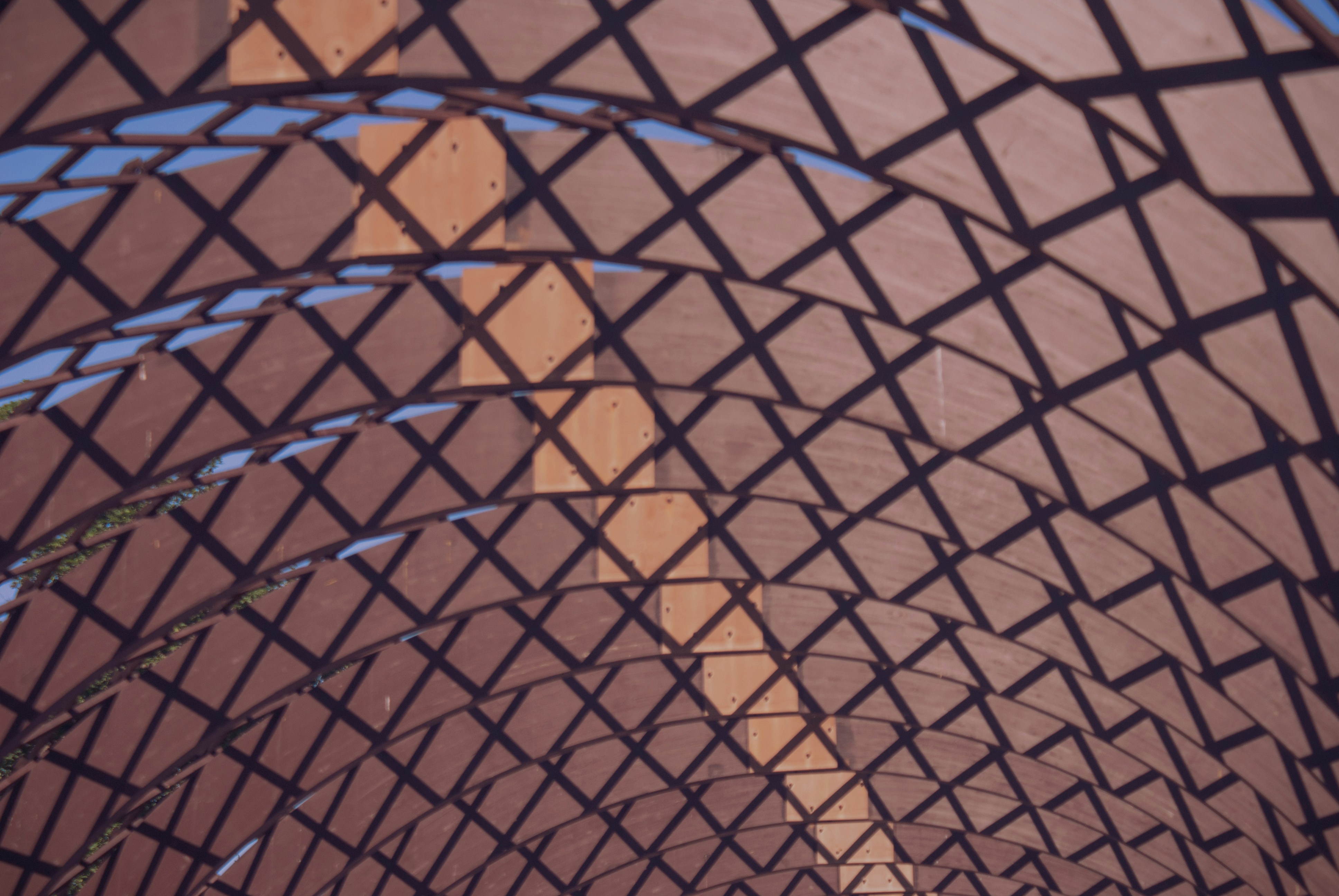 Wooden lattice structure casting intricate shadows against a clear blue sky.