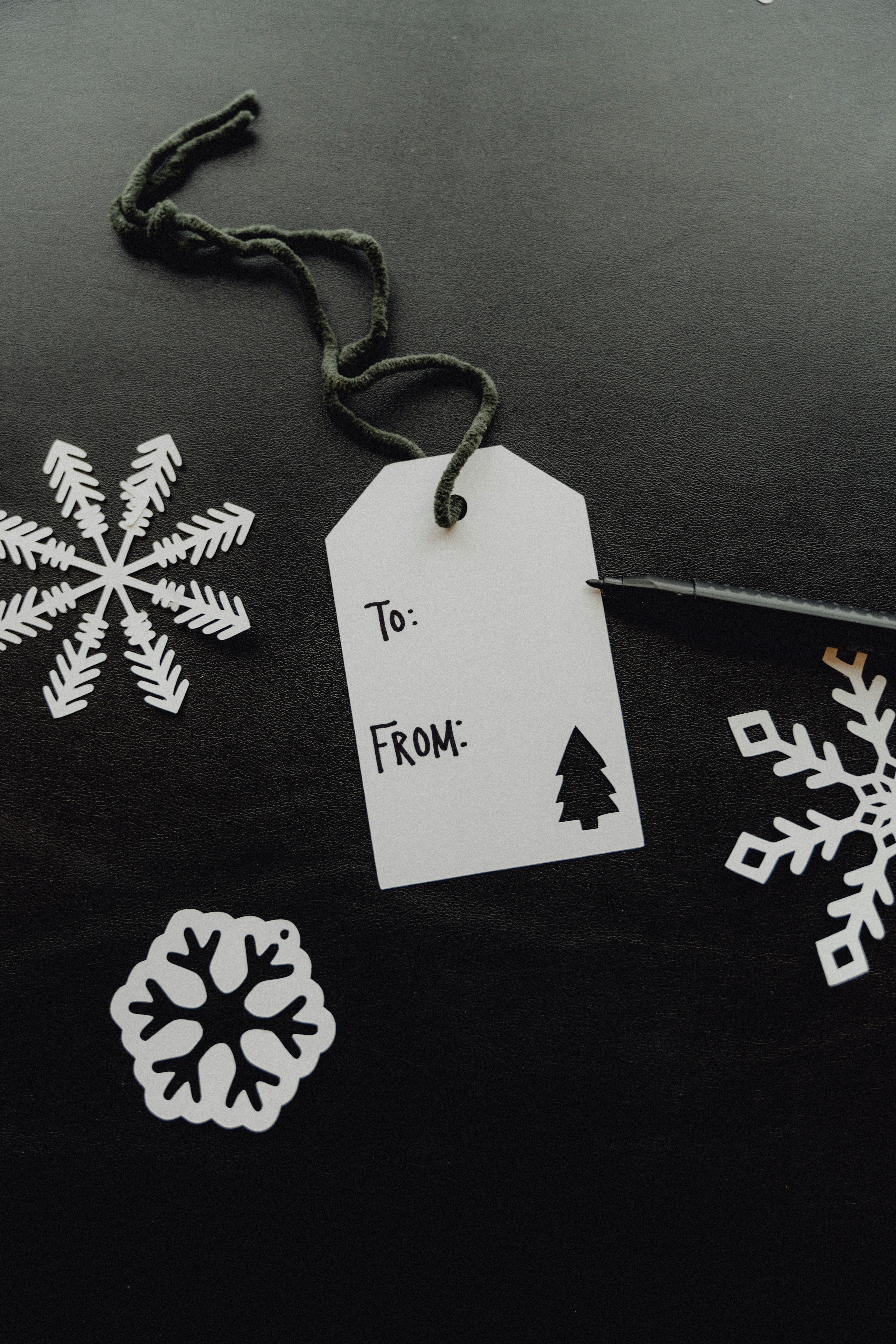 Gift tag with 'To' and 'From' fields beside paper snowflake decorations on a dark background.