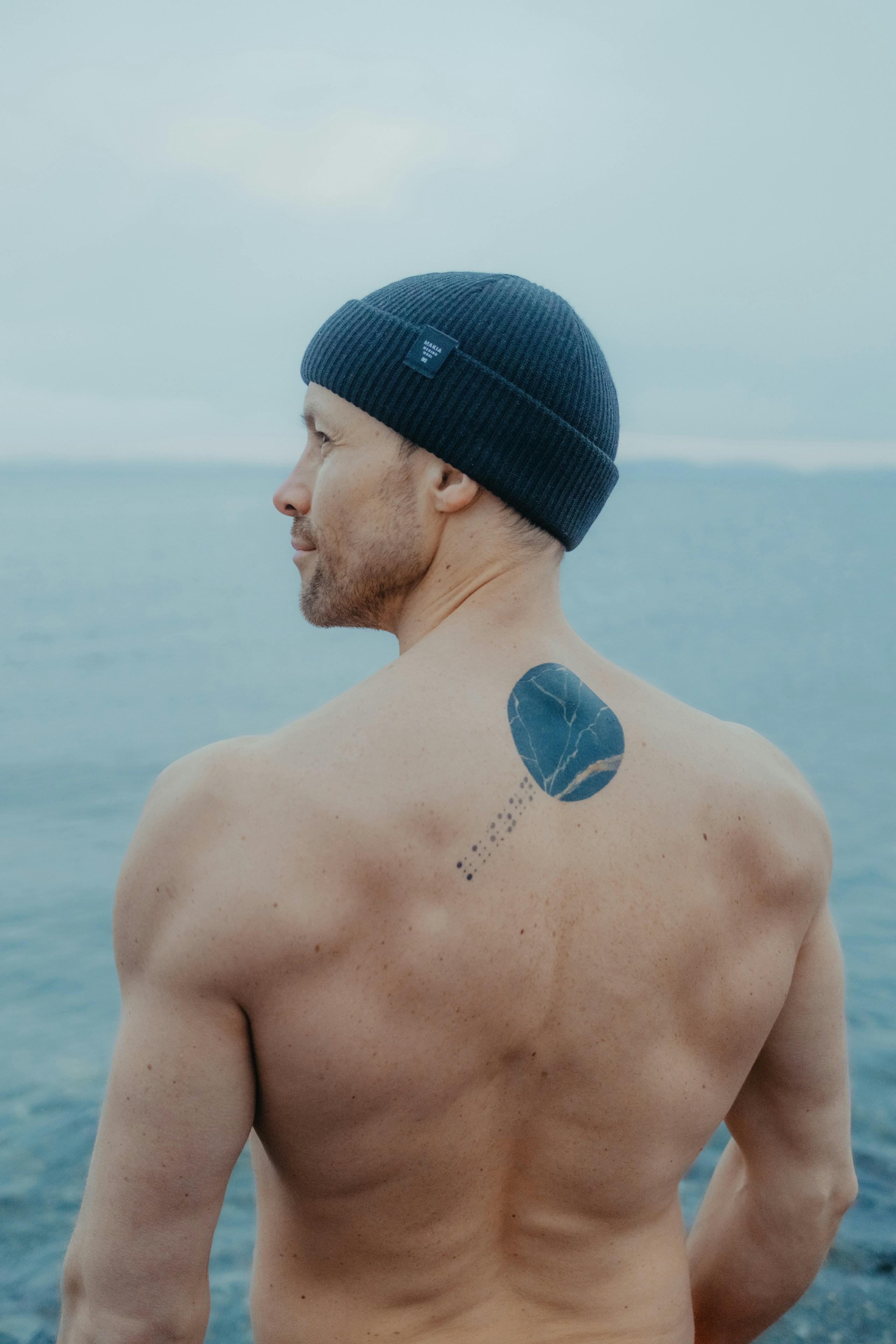 A man with a tattoo on his back standing next to the ocean photo – Free ...