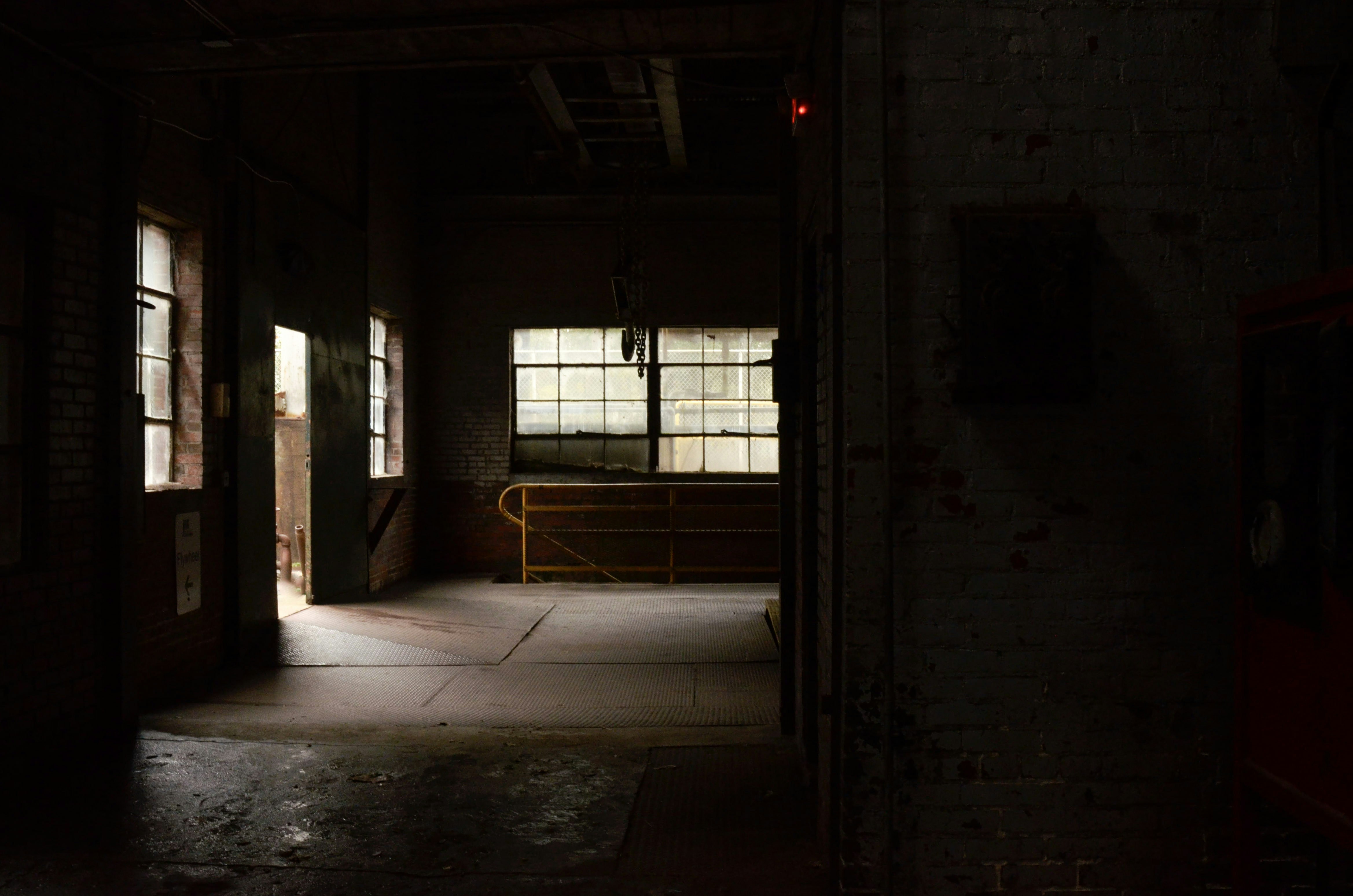 Dimly lit room with a wooden bench and large windows casting soft light.