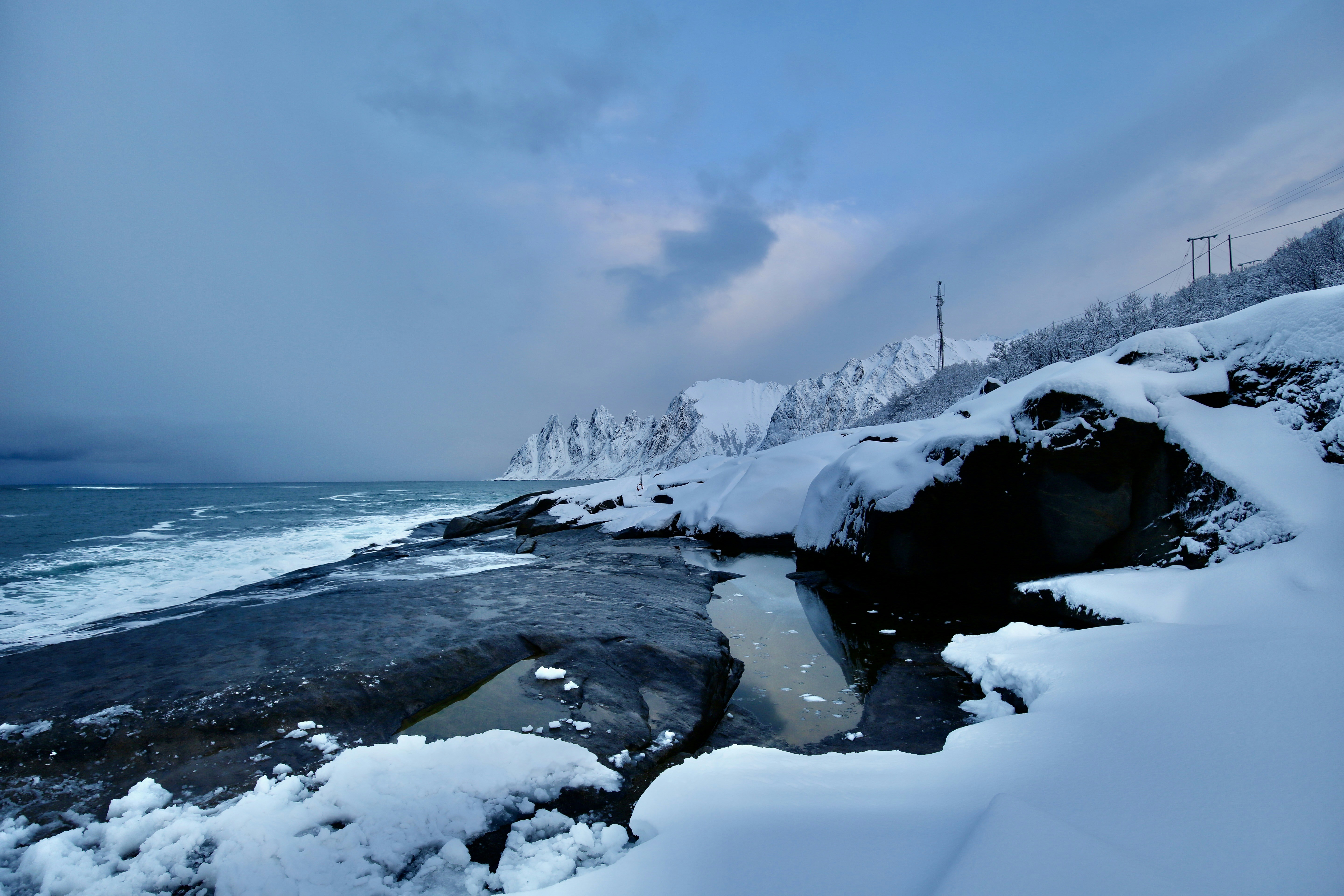 A rocky shore covered in snow next to the ocean photo – Free Senja ...