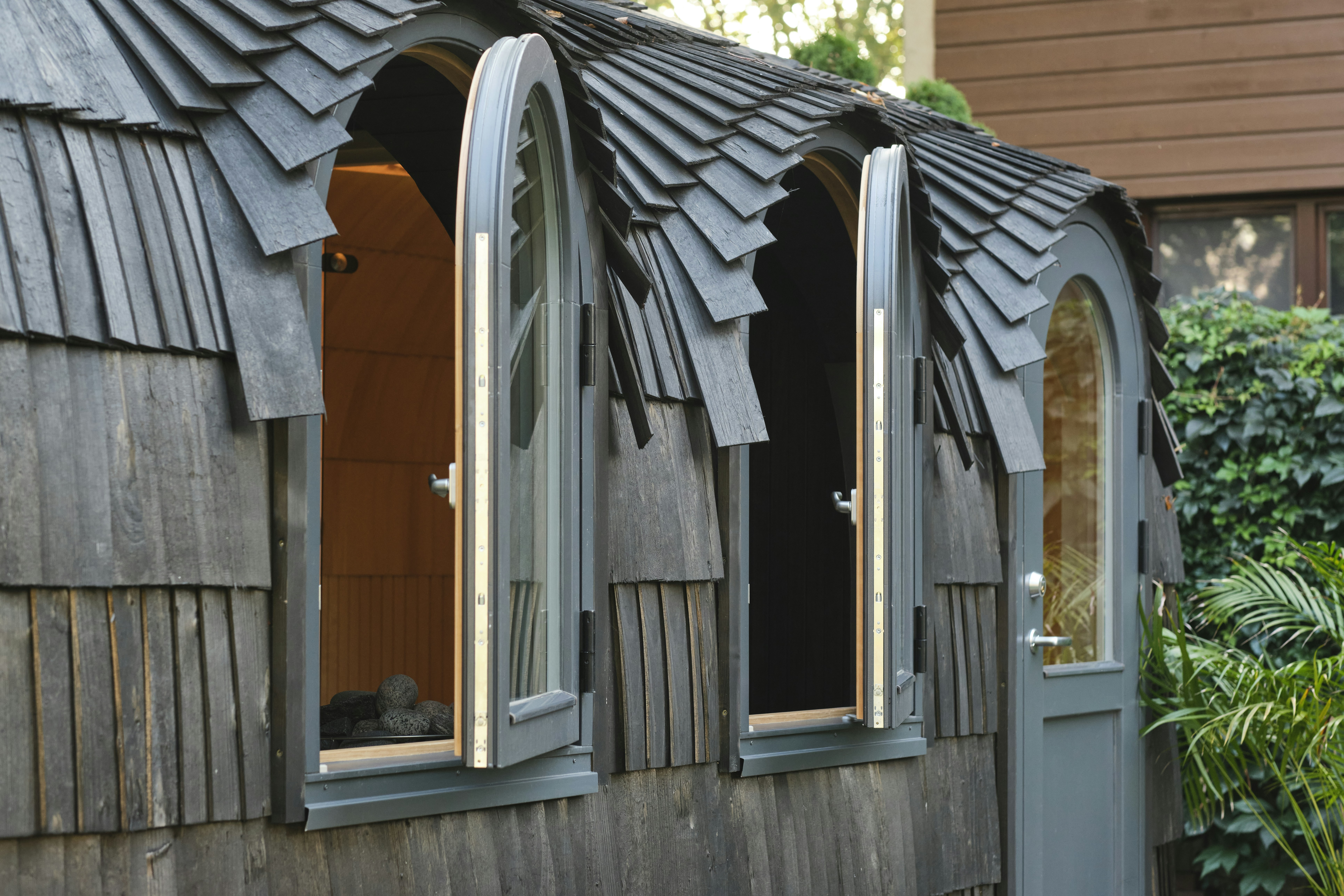 A uniquely designed cabin with arched windows and a textured wooden exterior, nestled among greenery. The architecture blends seamlessly with its natural surroundings.