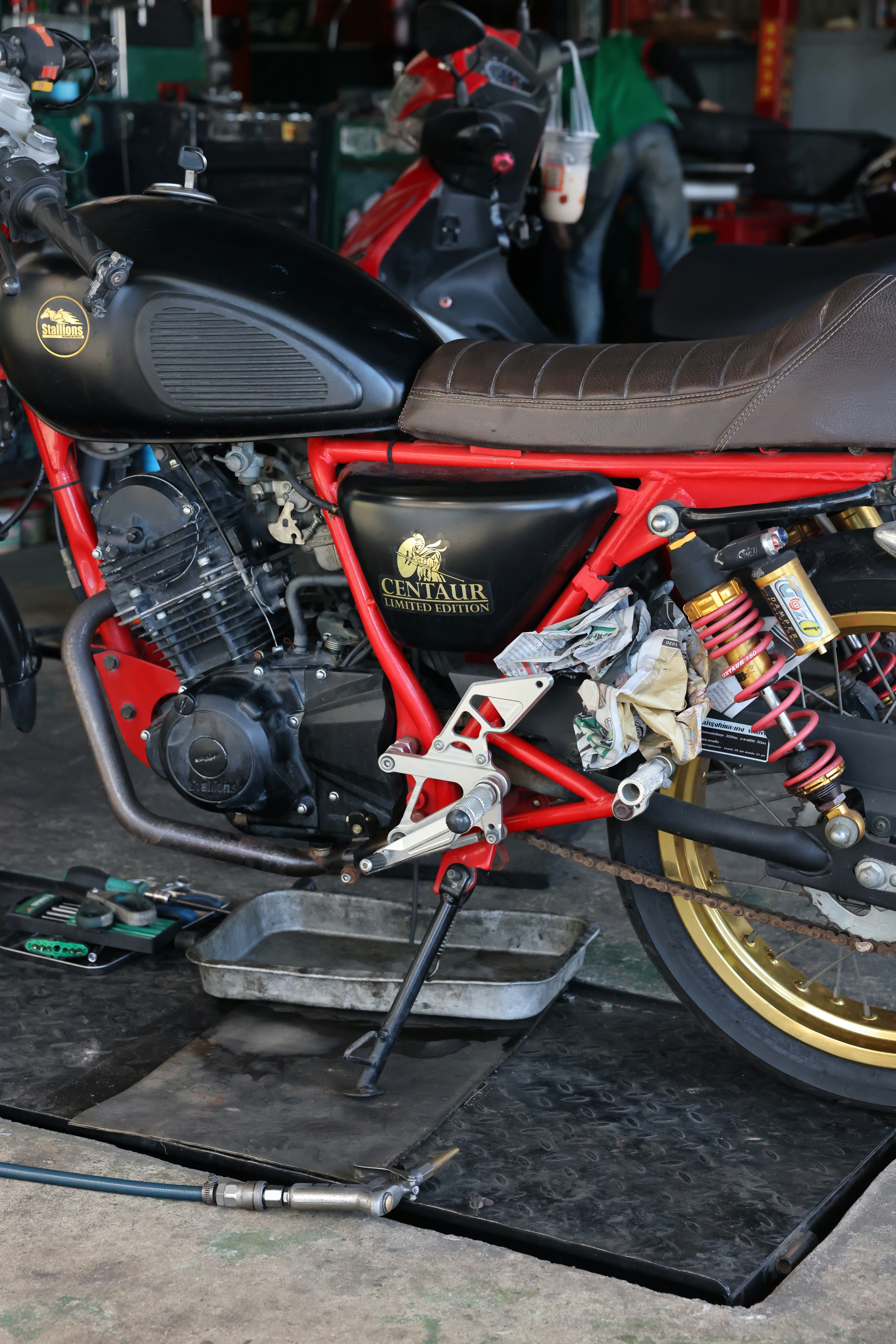 Close-up of a limited edition Centaur motorcycle in a workshop, showcasing its unique design and detailing. Tools and parts are scattered nearby, emphasizing the ongoing maintenance work.