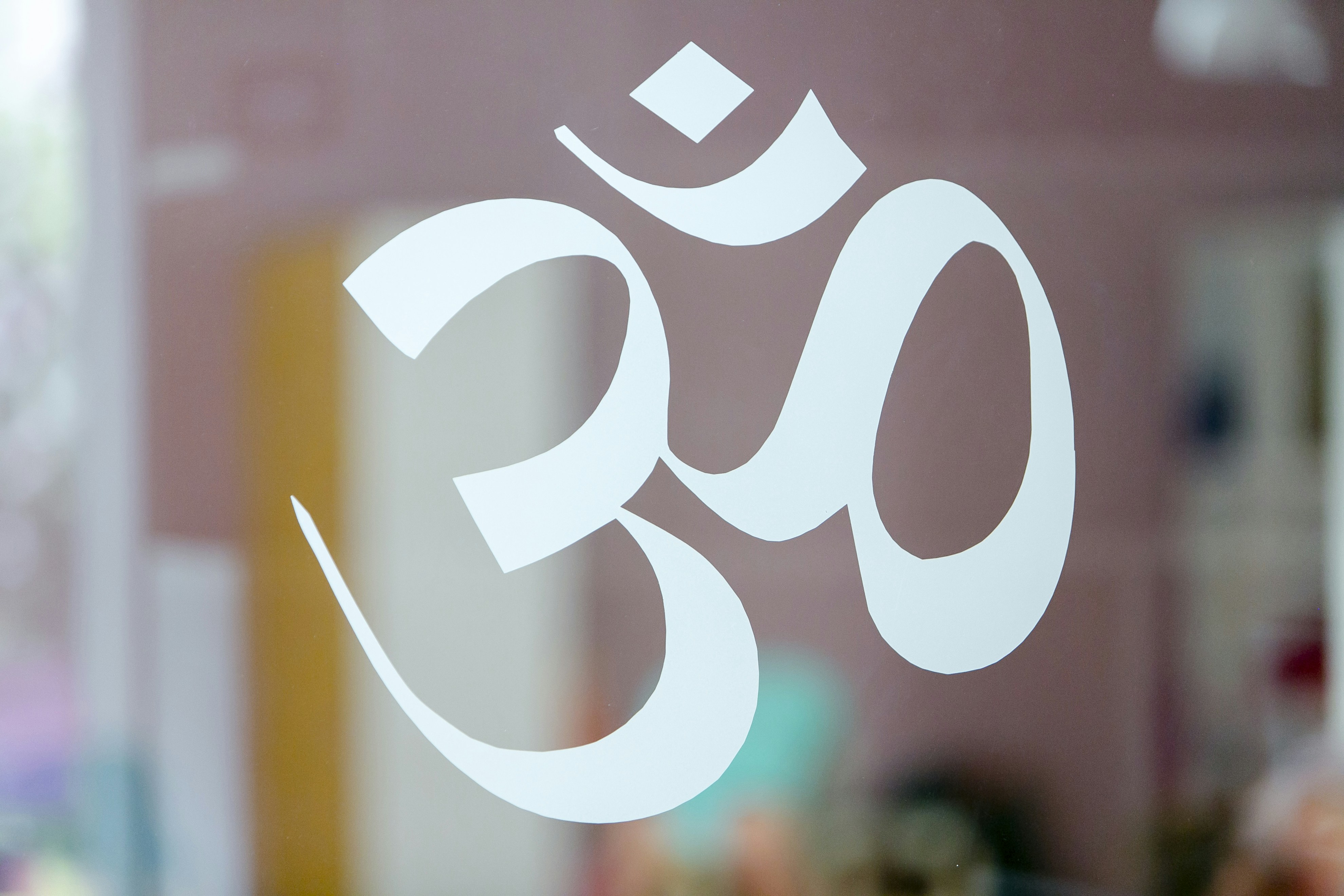 White Om symbol on a glass surface with a softly blurred background.
