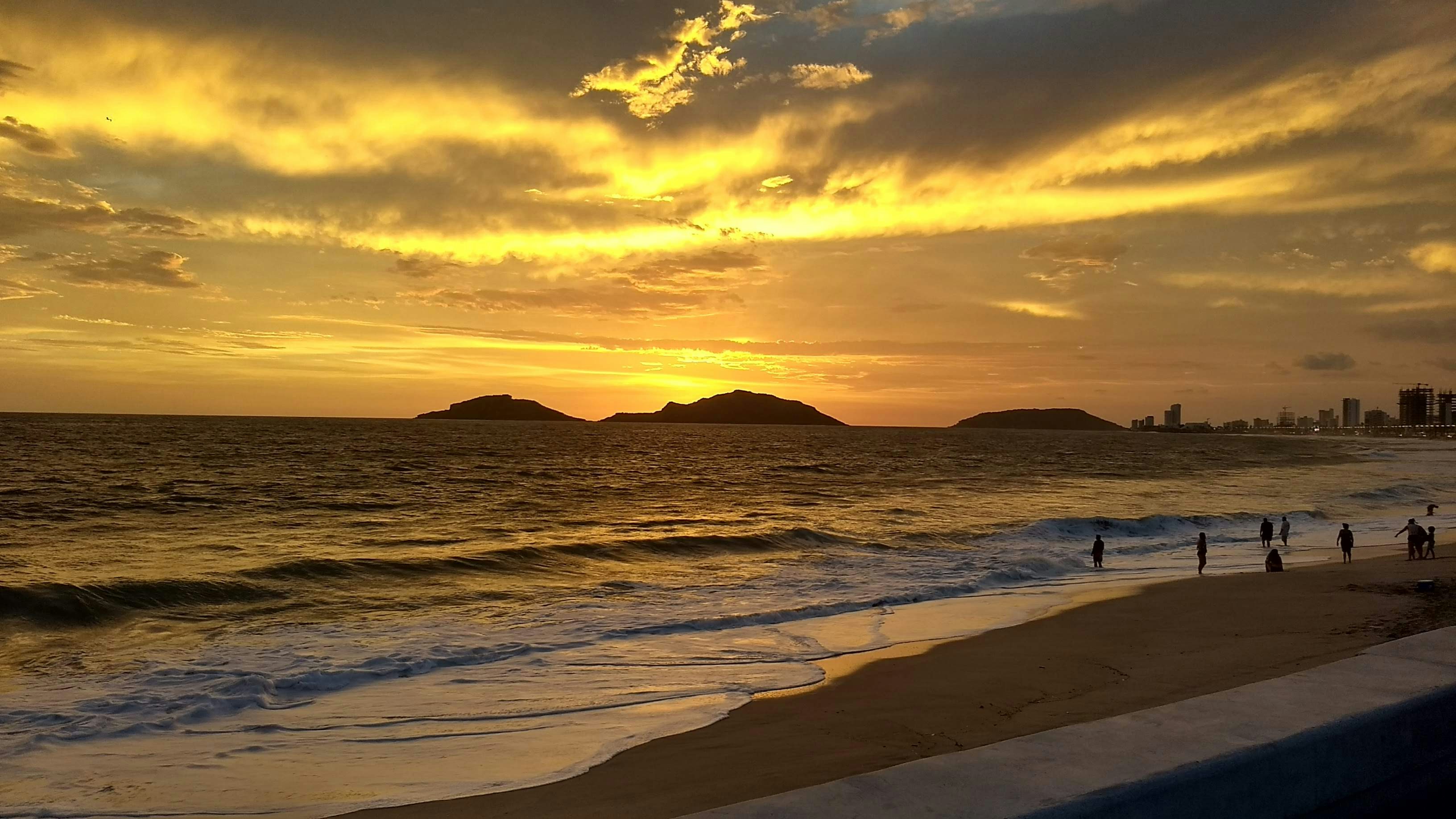Sunset casting golden hues over a tranquil beach with distant islands on the horizon.