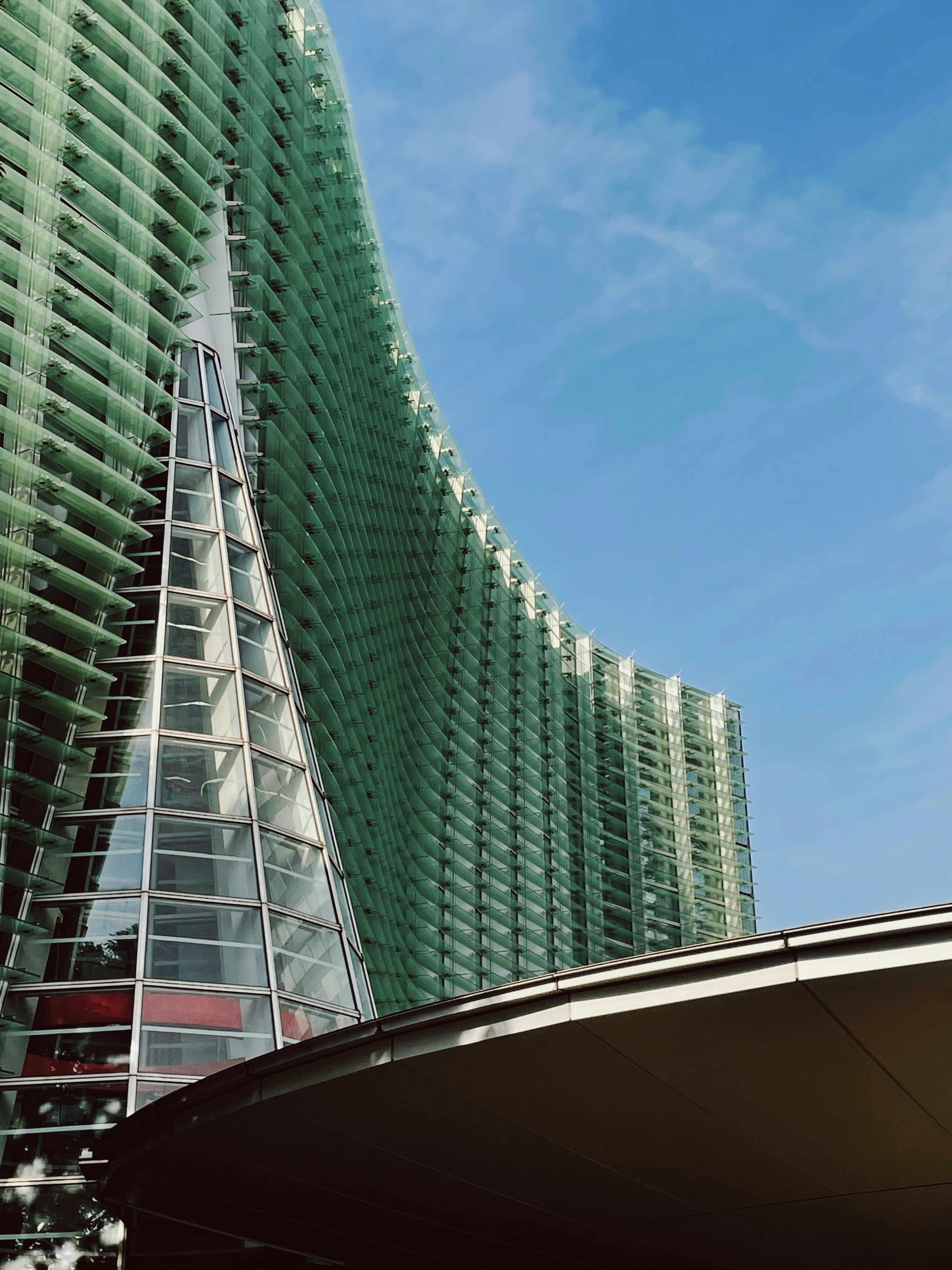 Curving glass skyline: a green-tinted tower rises against a clear blue sky