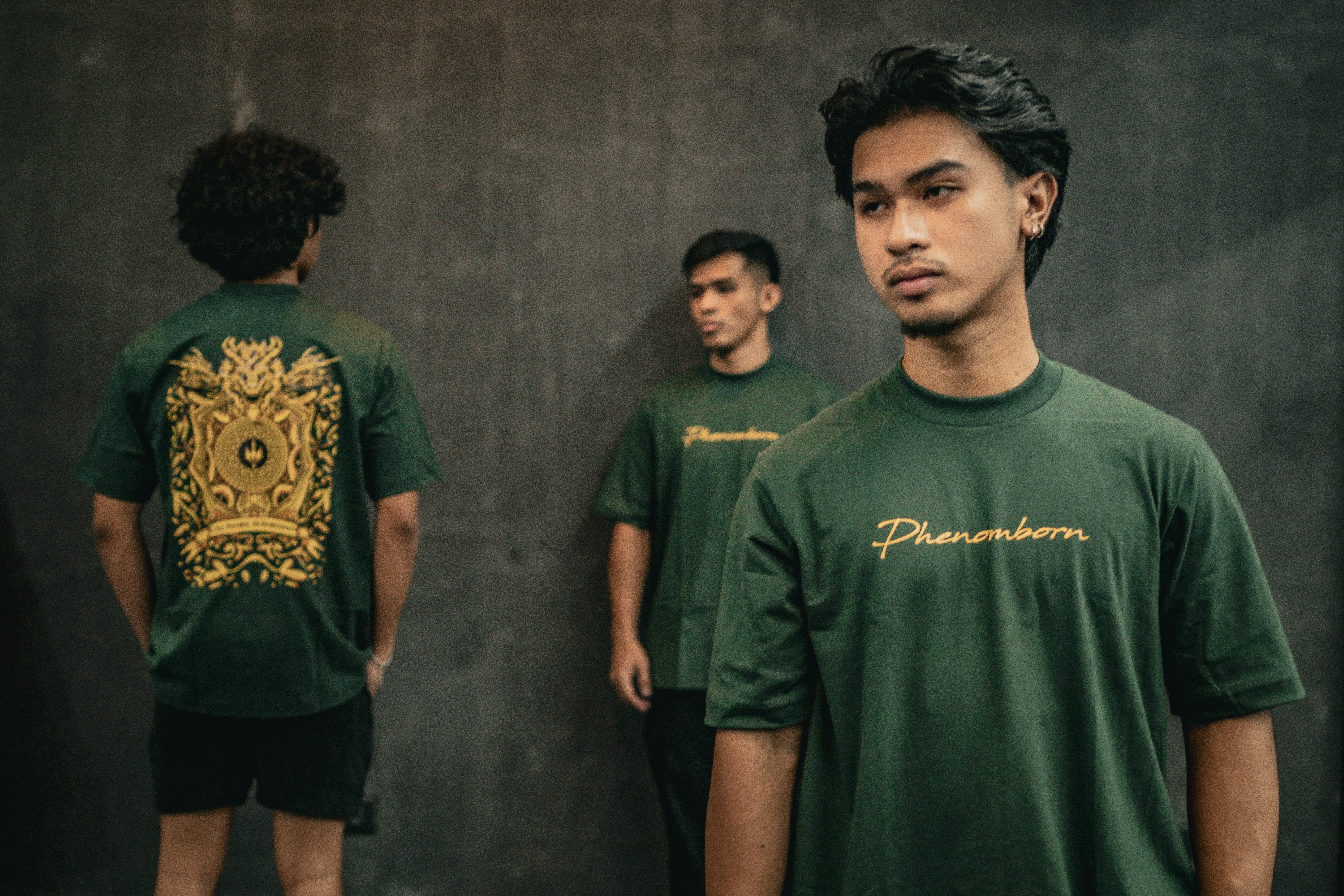 Rightmost Focus: A Quiet Trio in Green Tees Against a Dim Studio Wall