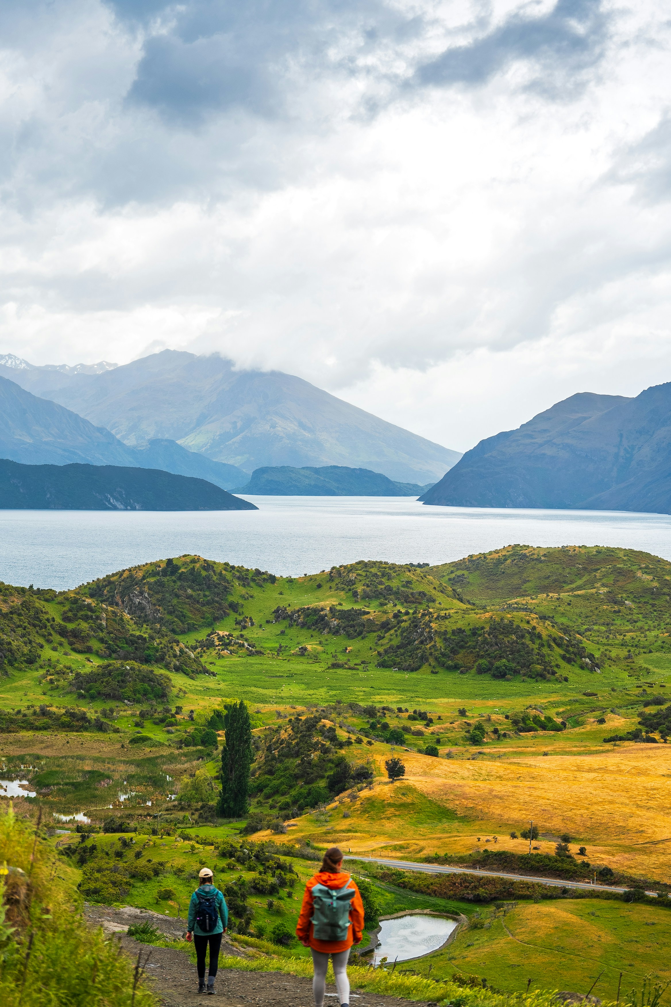 Hikers Reaching the Ridge: A Quiet Trek Across Verdant Hills by a Mountain Lake