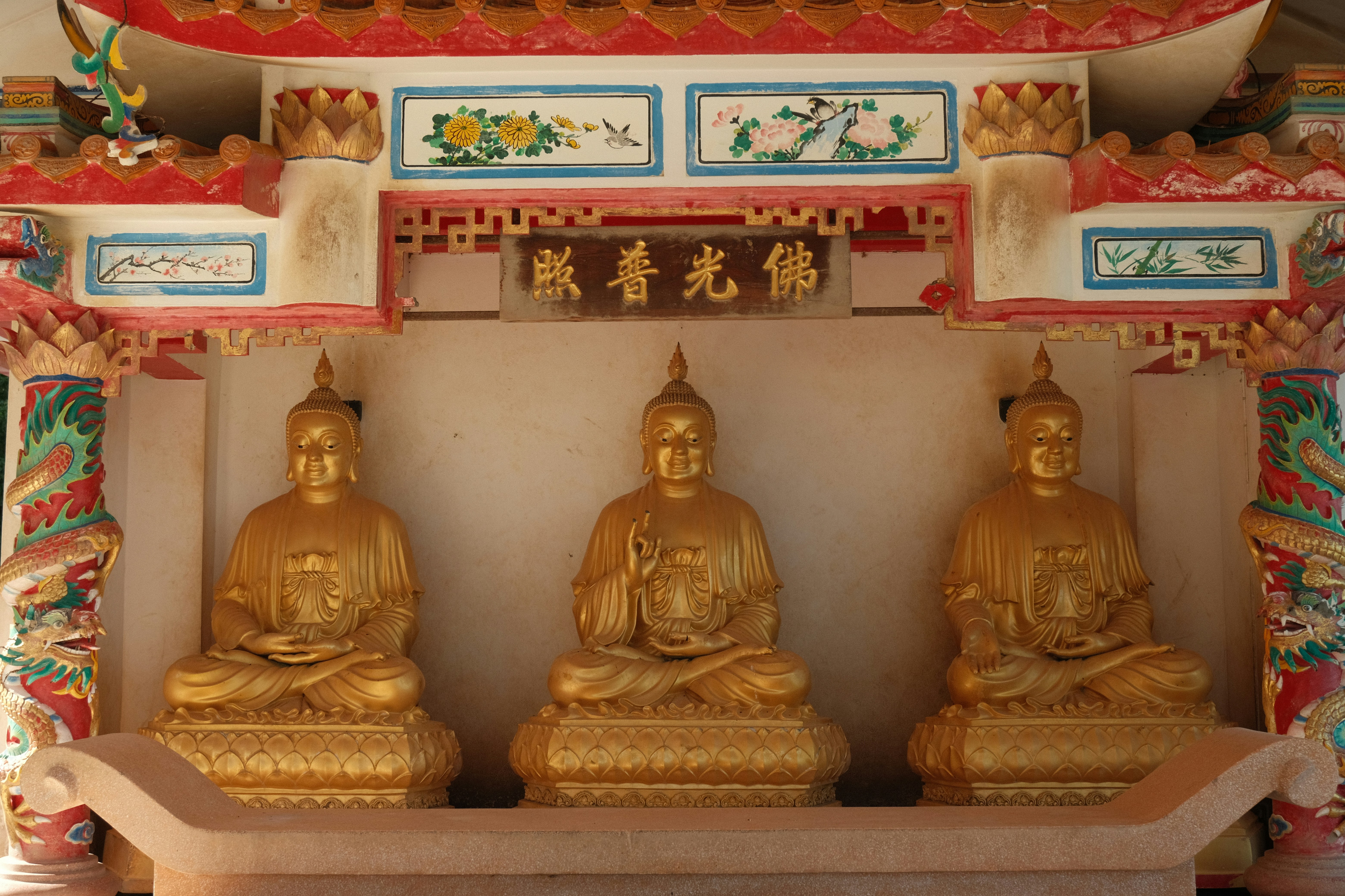 Three golden Buddha statues seated in a richly decorated shrine with intricate patterns and vibrant colors.