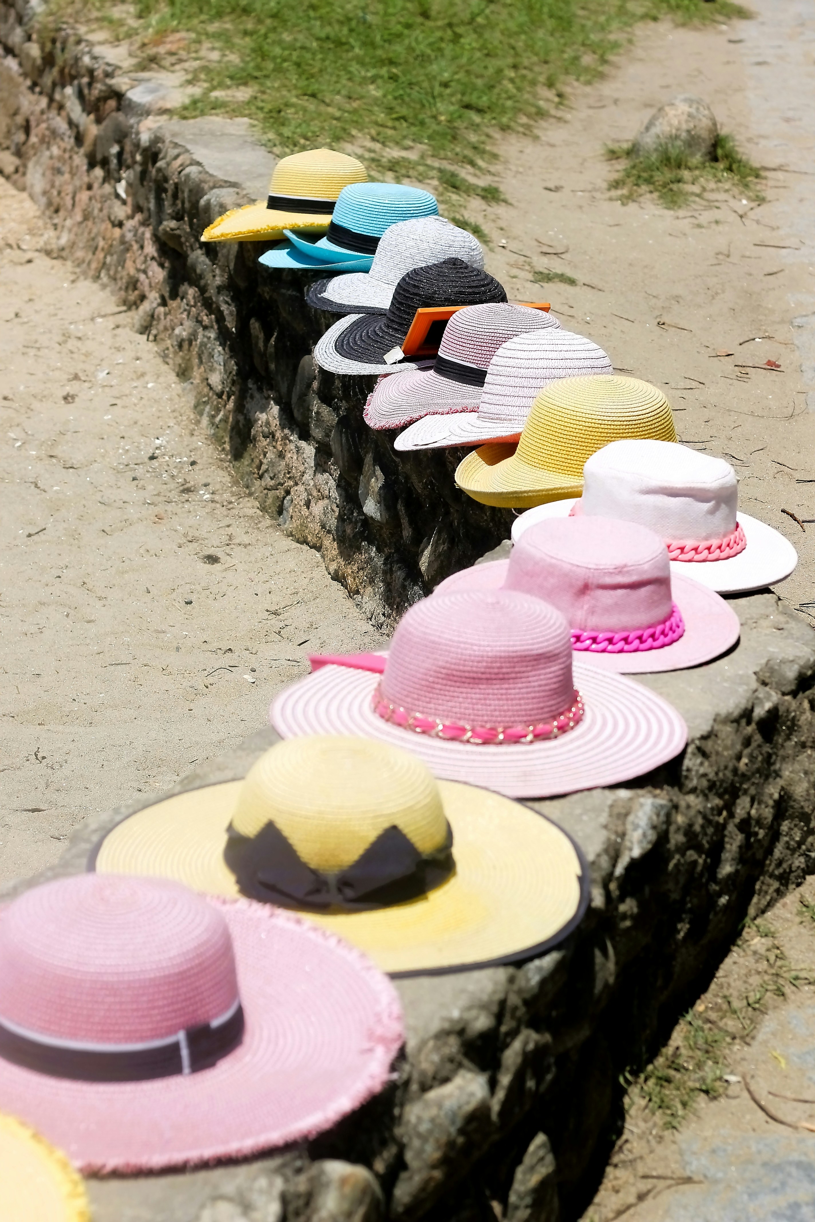 Pastel Parade: Hats Line Up Along a Sunlit Seawall