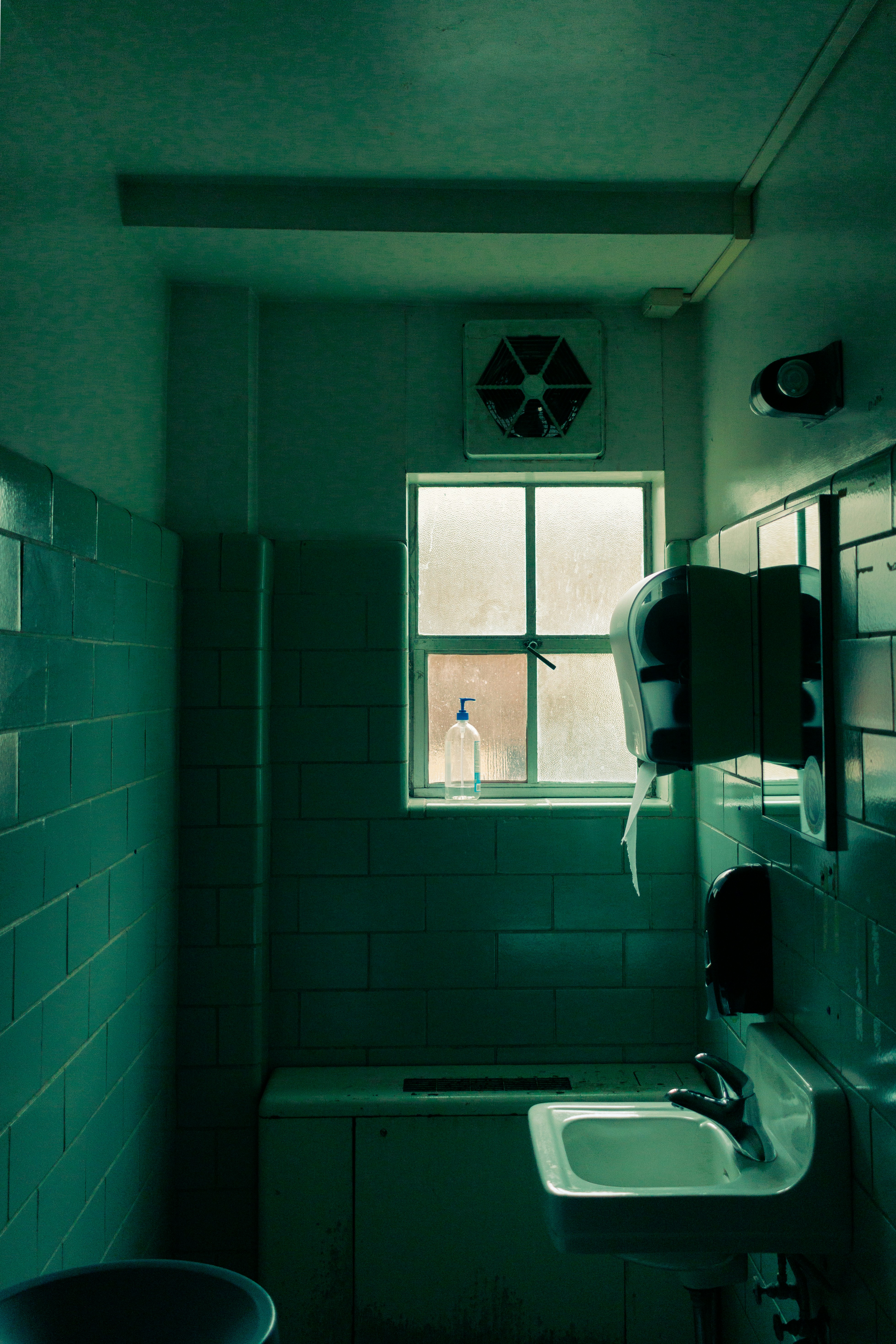 Dimly lit restroom with teal tiles and a small window casting soft light.