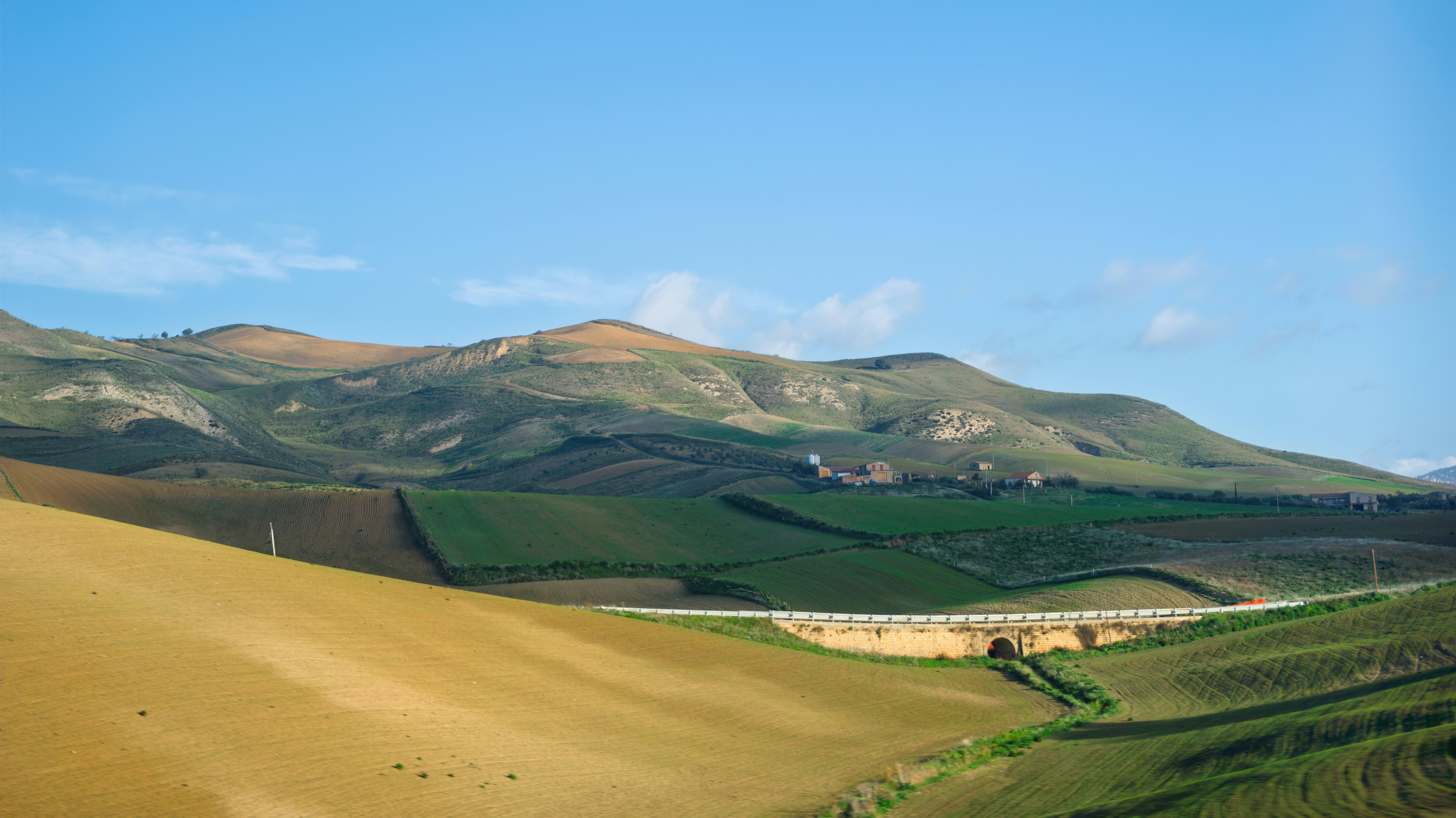 Rolling hills with golden and green fields under a clear blue sky.