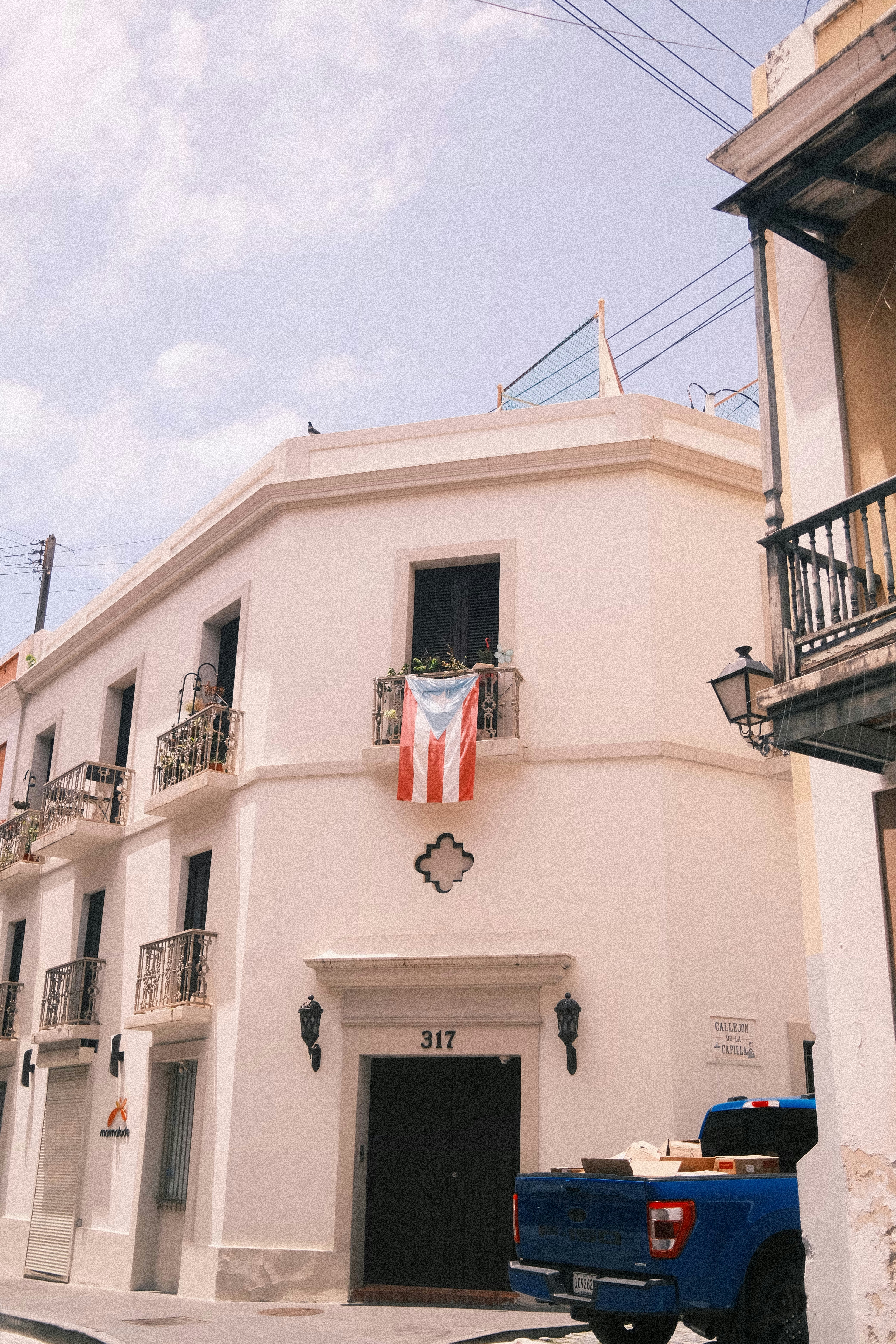 Flag on a sunlit colonial balcony anchors a quiet pastel street.