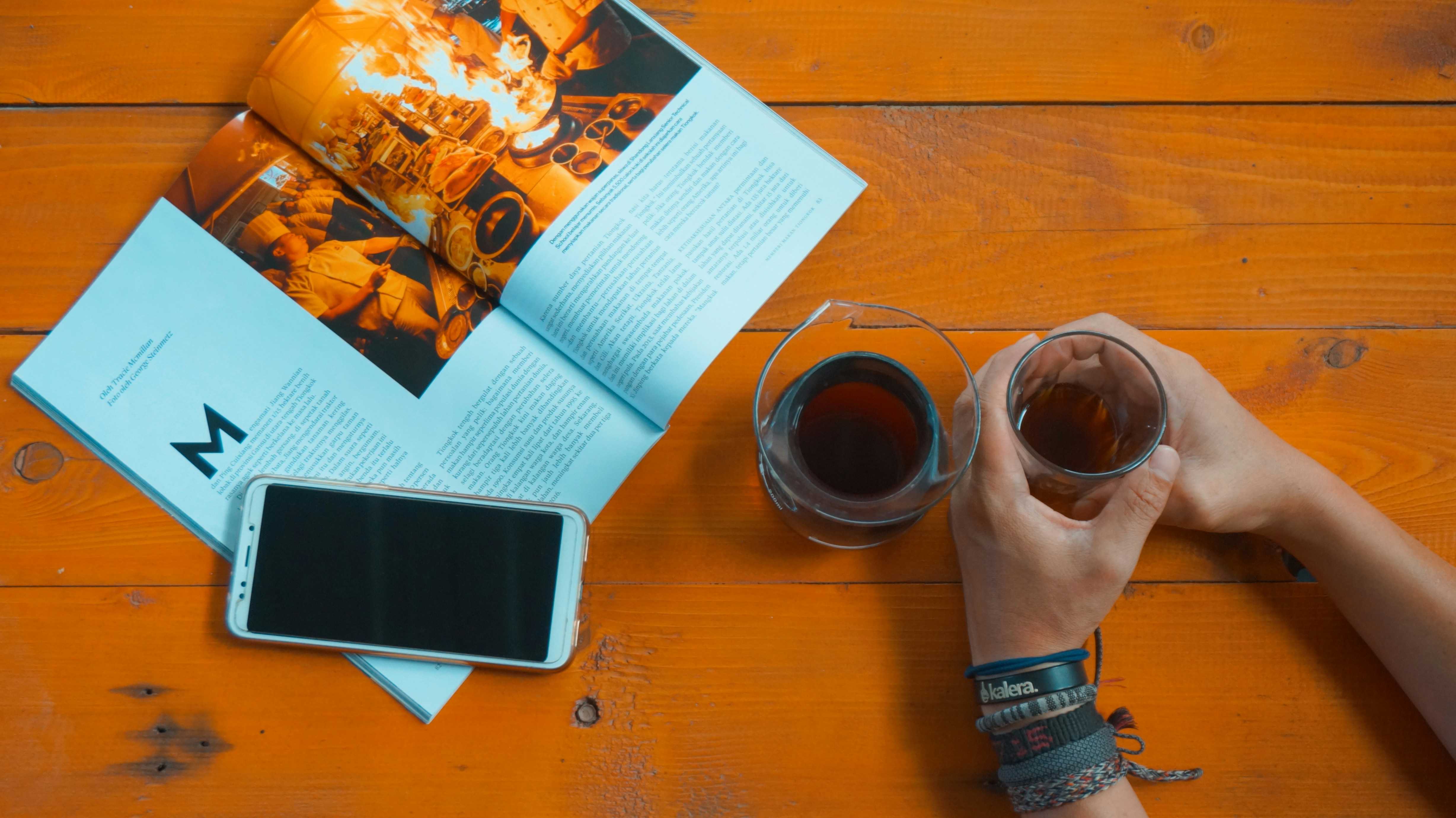 Clinking Glasses Over a Weekend Brew: A Magazine, Phone, and Wristbands on a Wooden Table