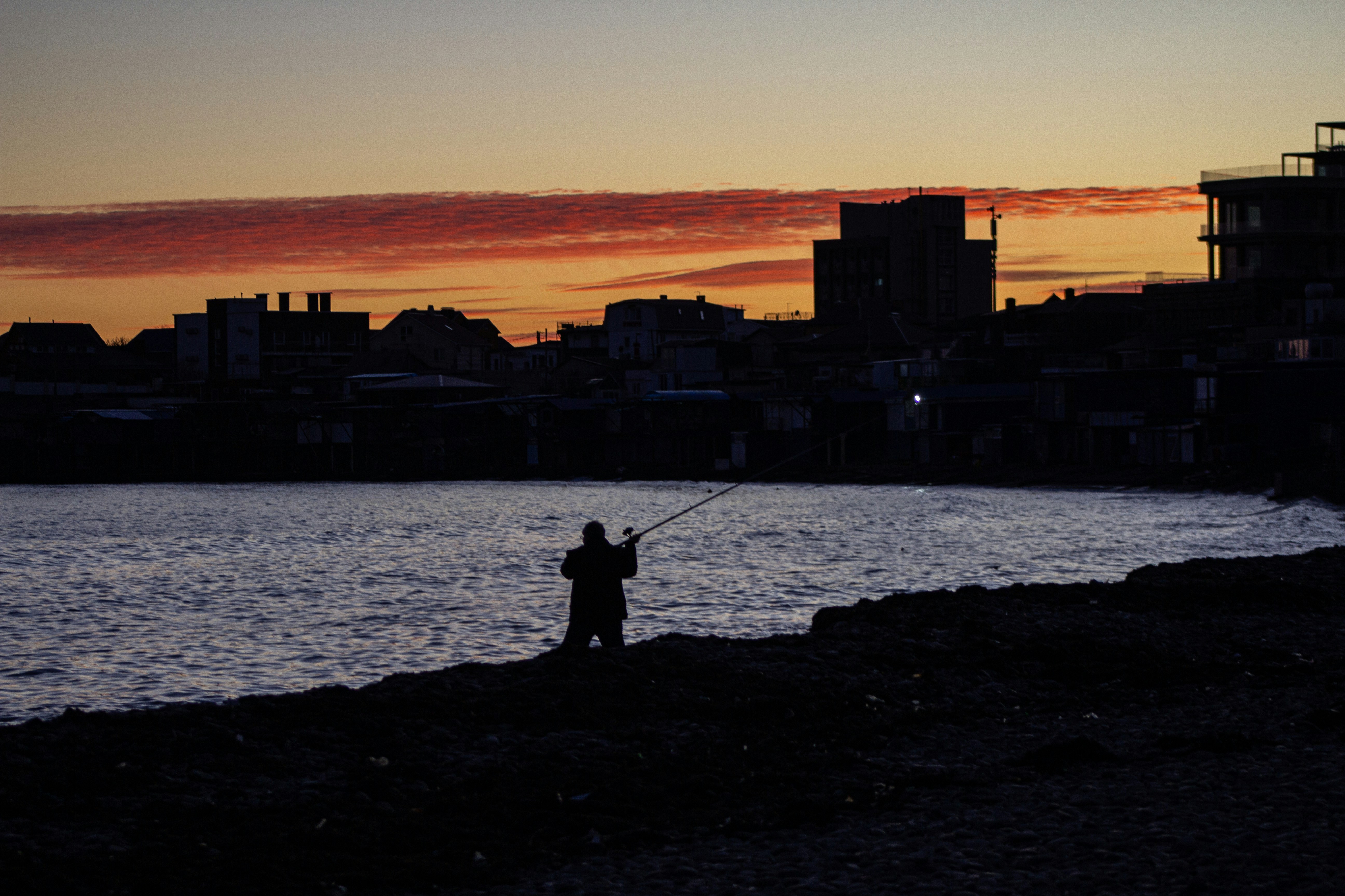 Dusk Silhouette: A Lone Angler Against the Red Horizon