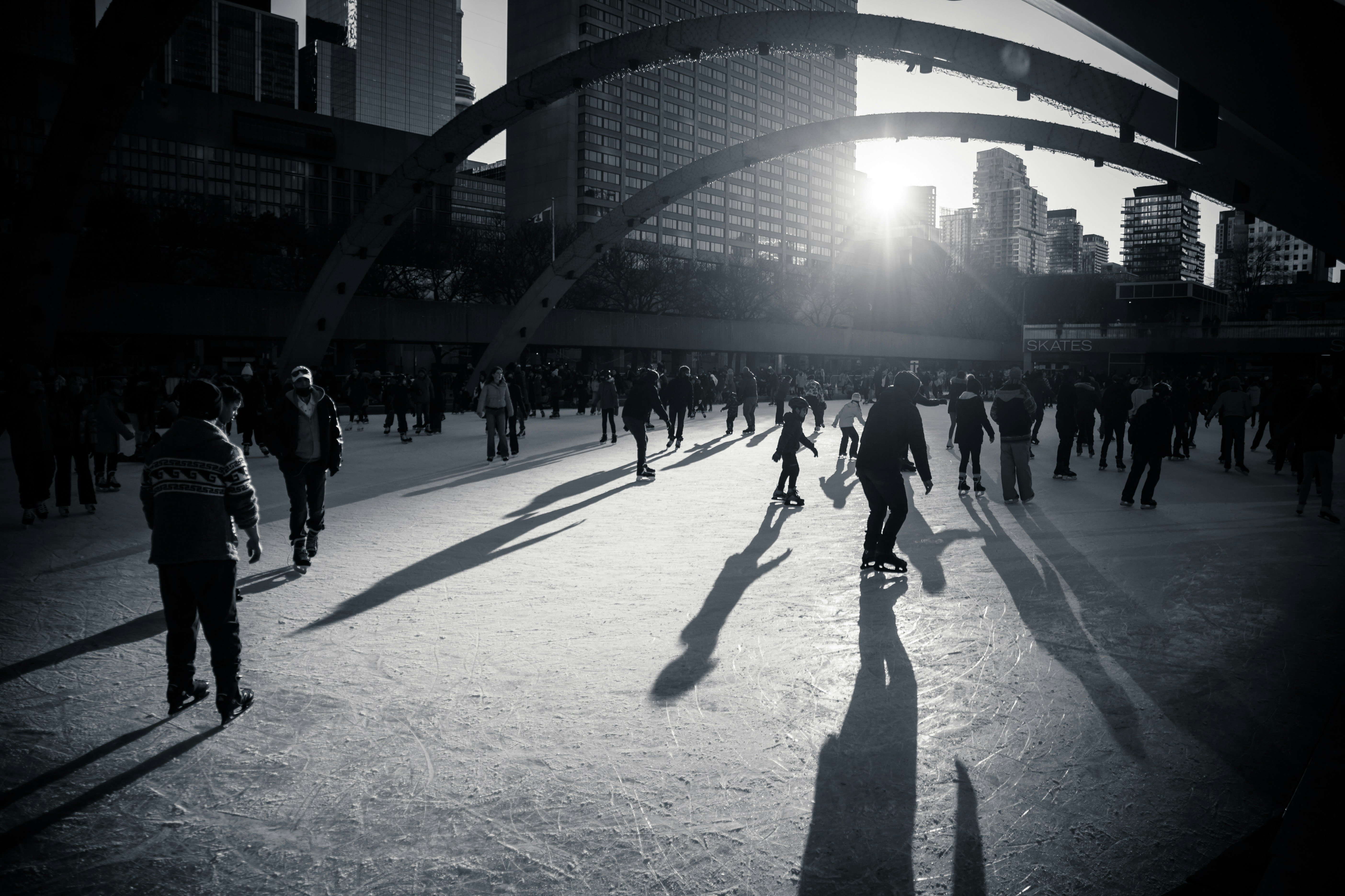 Urban Ice Ballet: Sunlit Shadows and City Arches Over a Frozen Rink