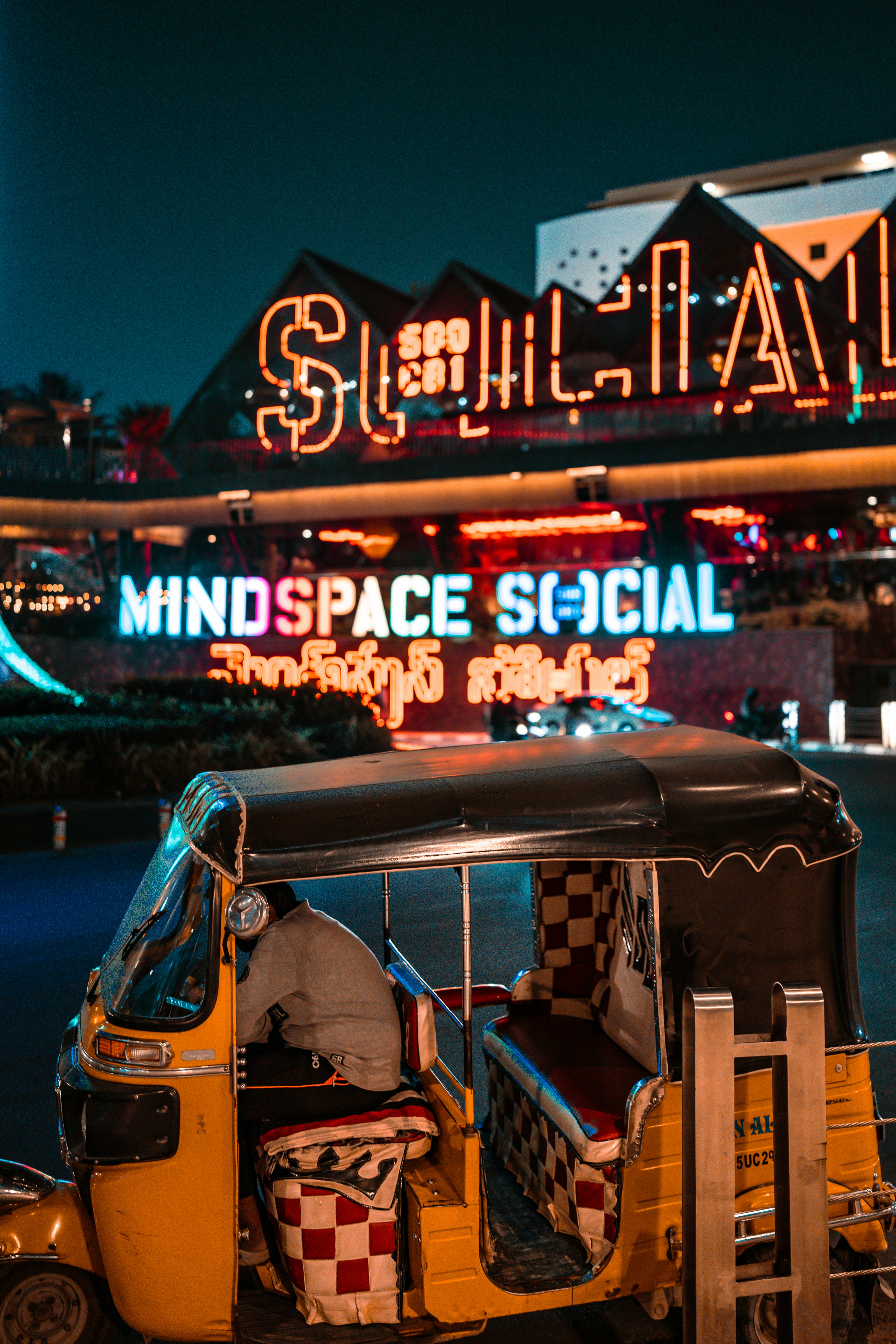 Yellow tuk tuk parked in front of vibrant neon signs at night.