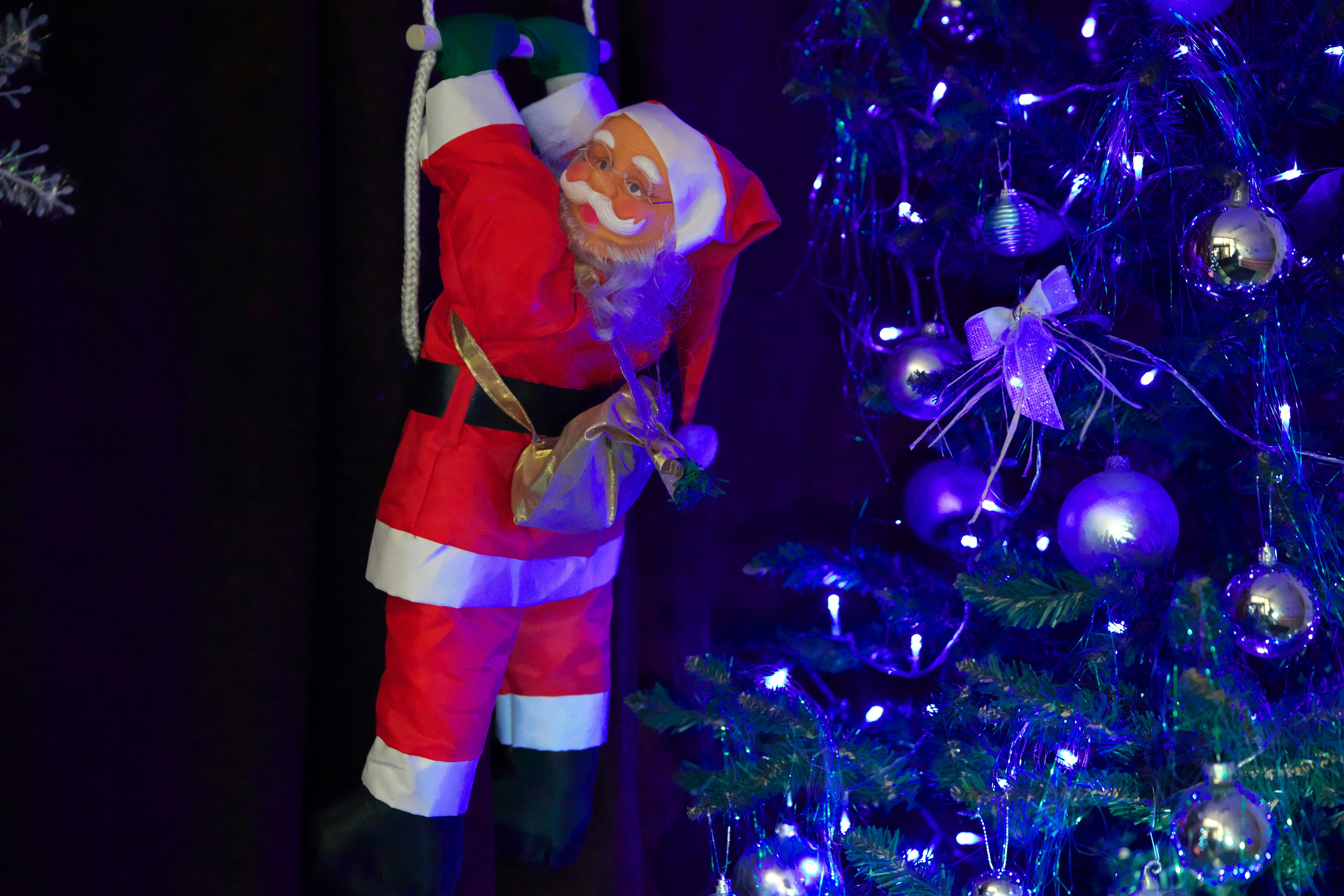 Santa Claus figure climbing near a Christmas tree adorned with blue lights and ornaments.