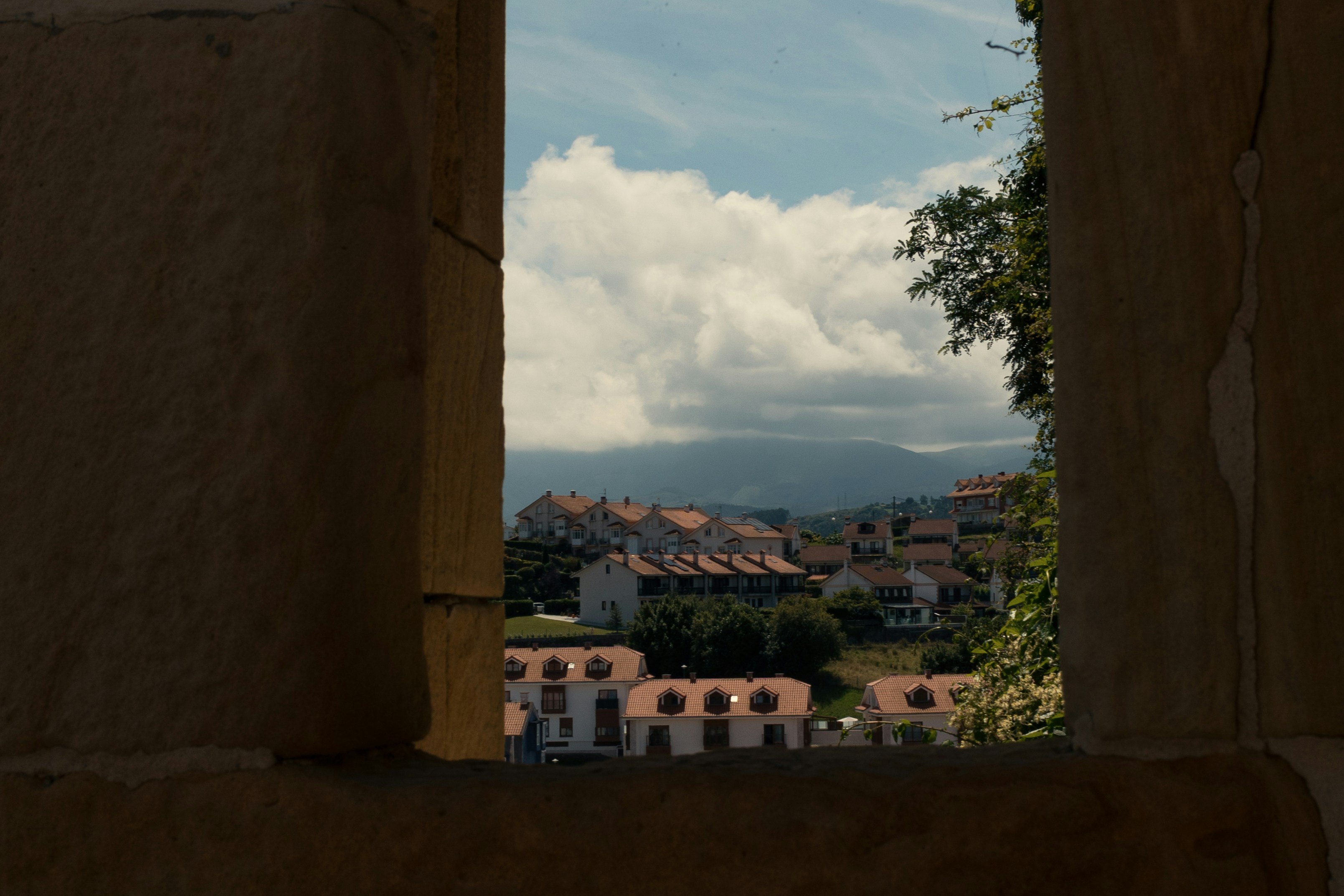 A scenic landscape captured through an ancient stone window, revealing charming rooftops and distant mountains under a cloudy sky.