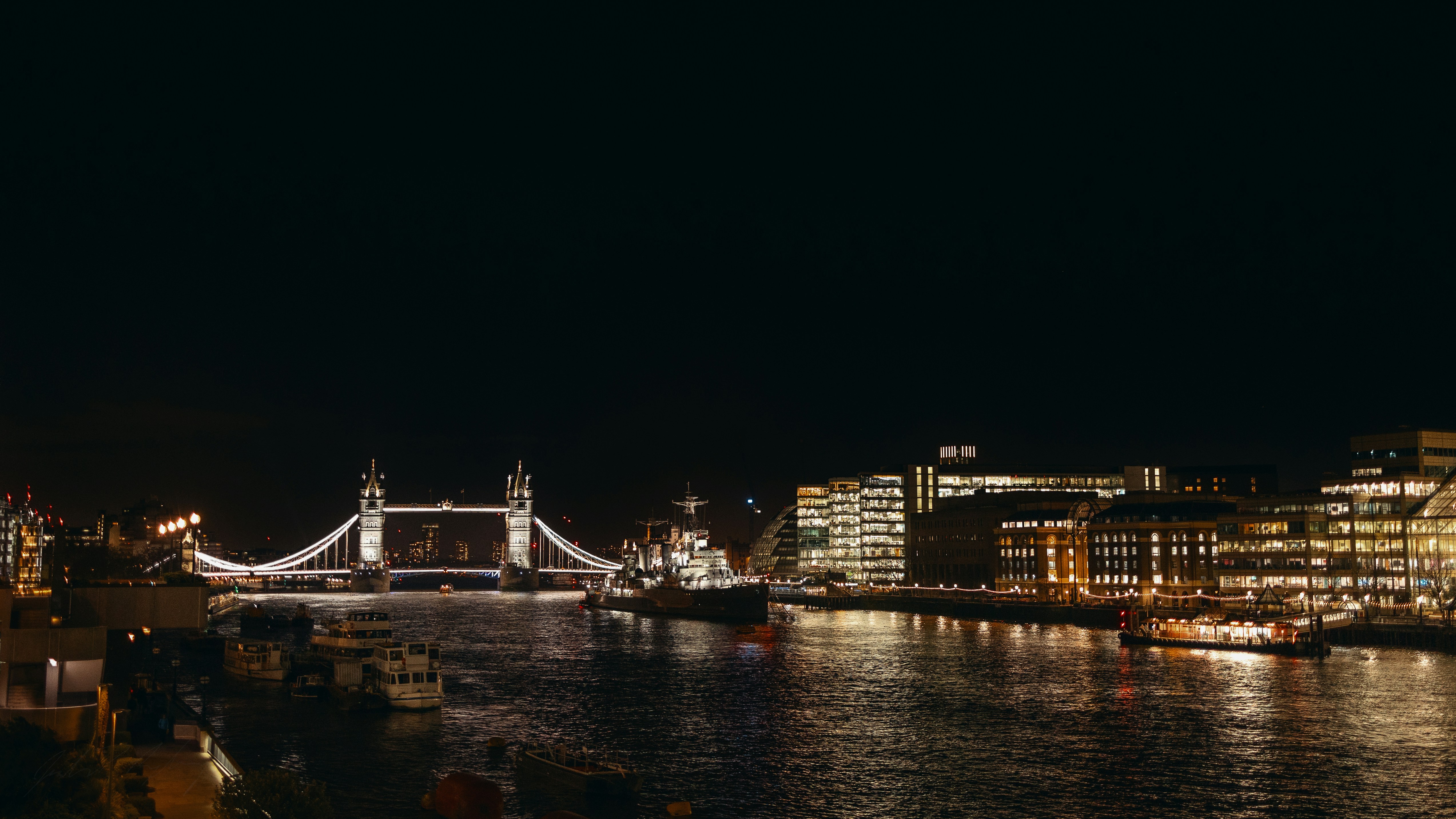 Tower Bridge and surrounding cityscape reflected in the Thames under night sky.