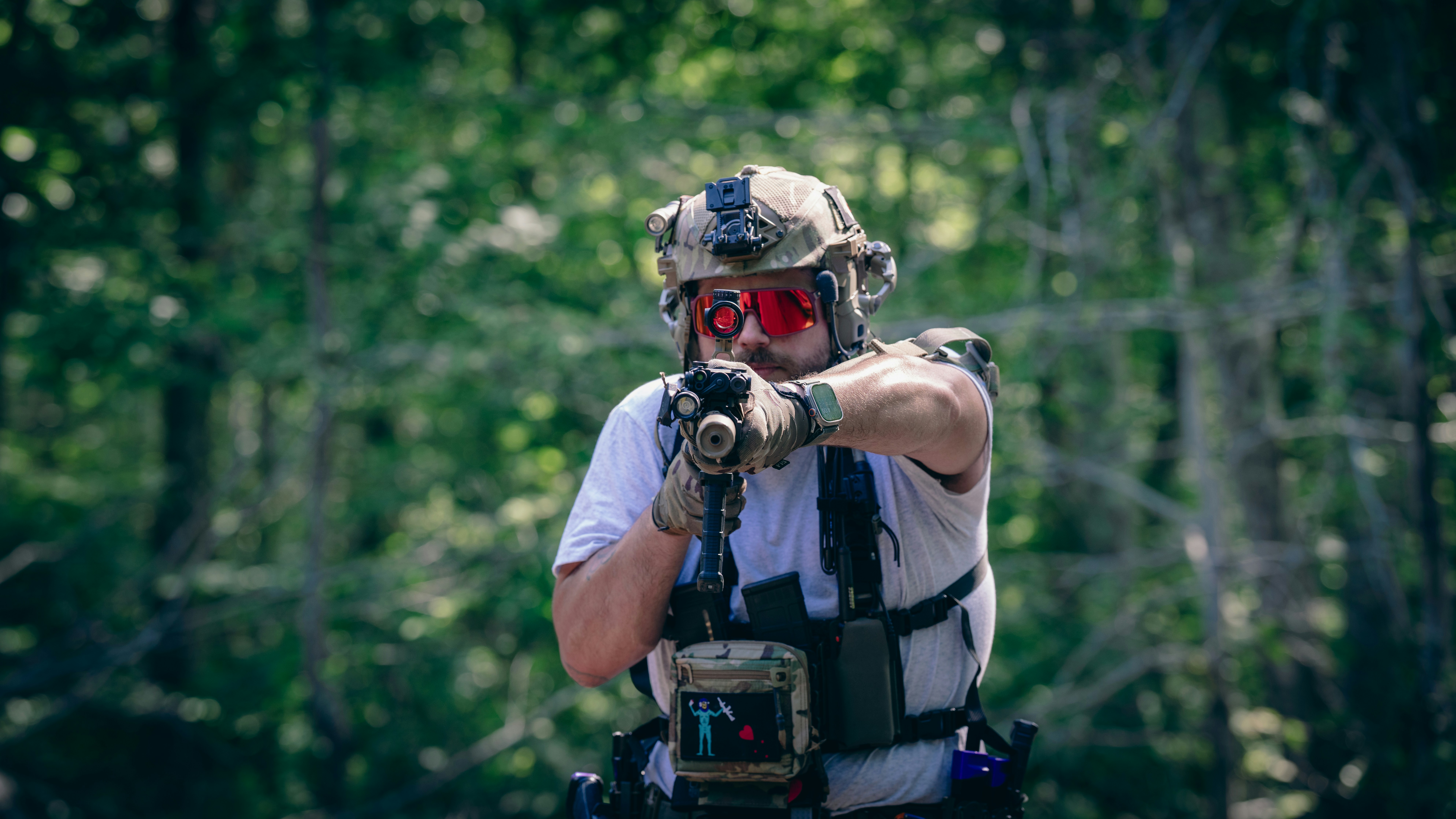 A tactical operator aims a firearm during a training exercise, showcasing focus and readiness in a wooded environment.