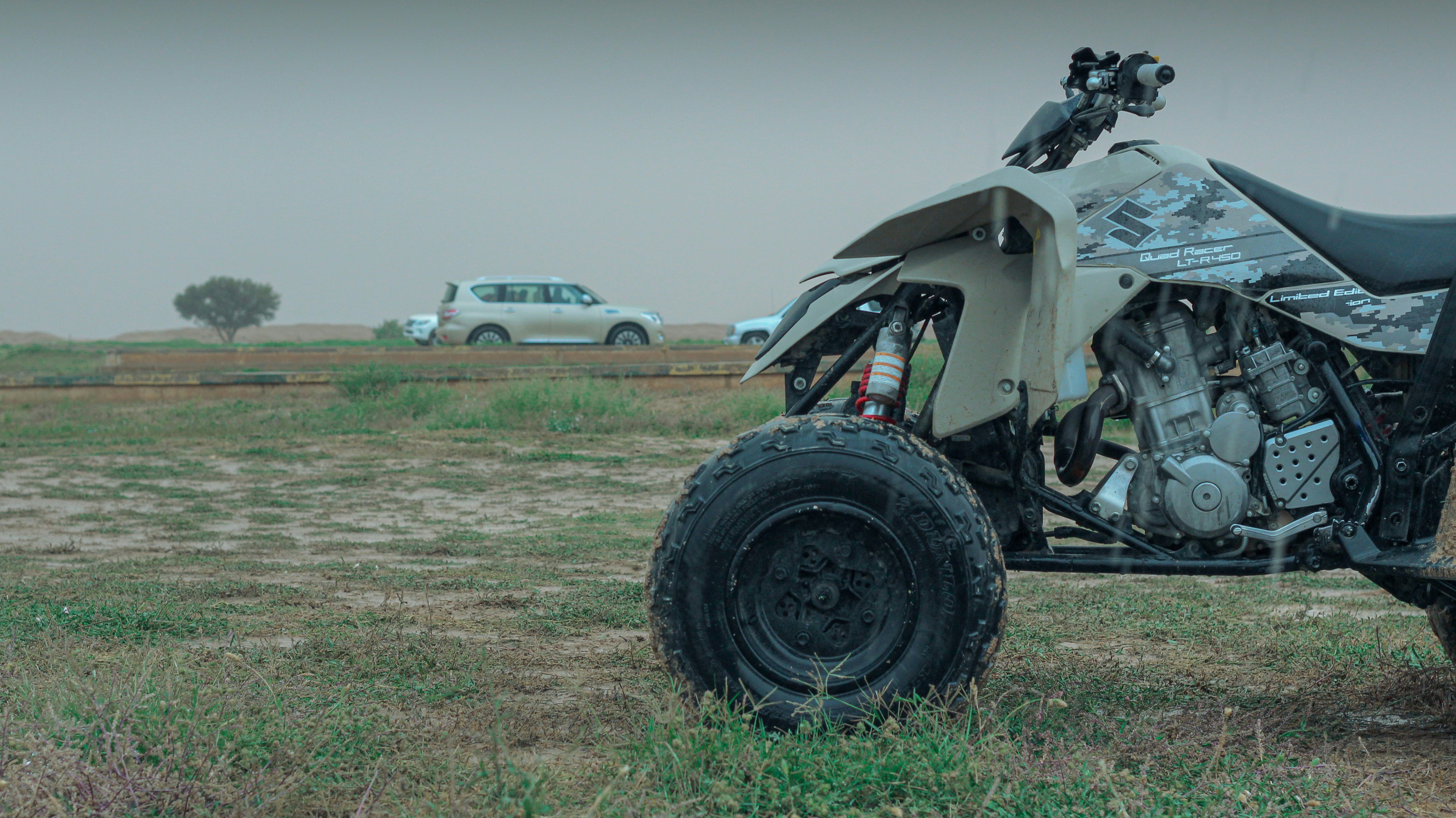Dusty field, looming quad bike, distant car—quiet showdown at the misshapen horizon