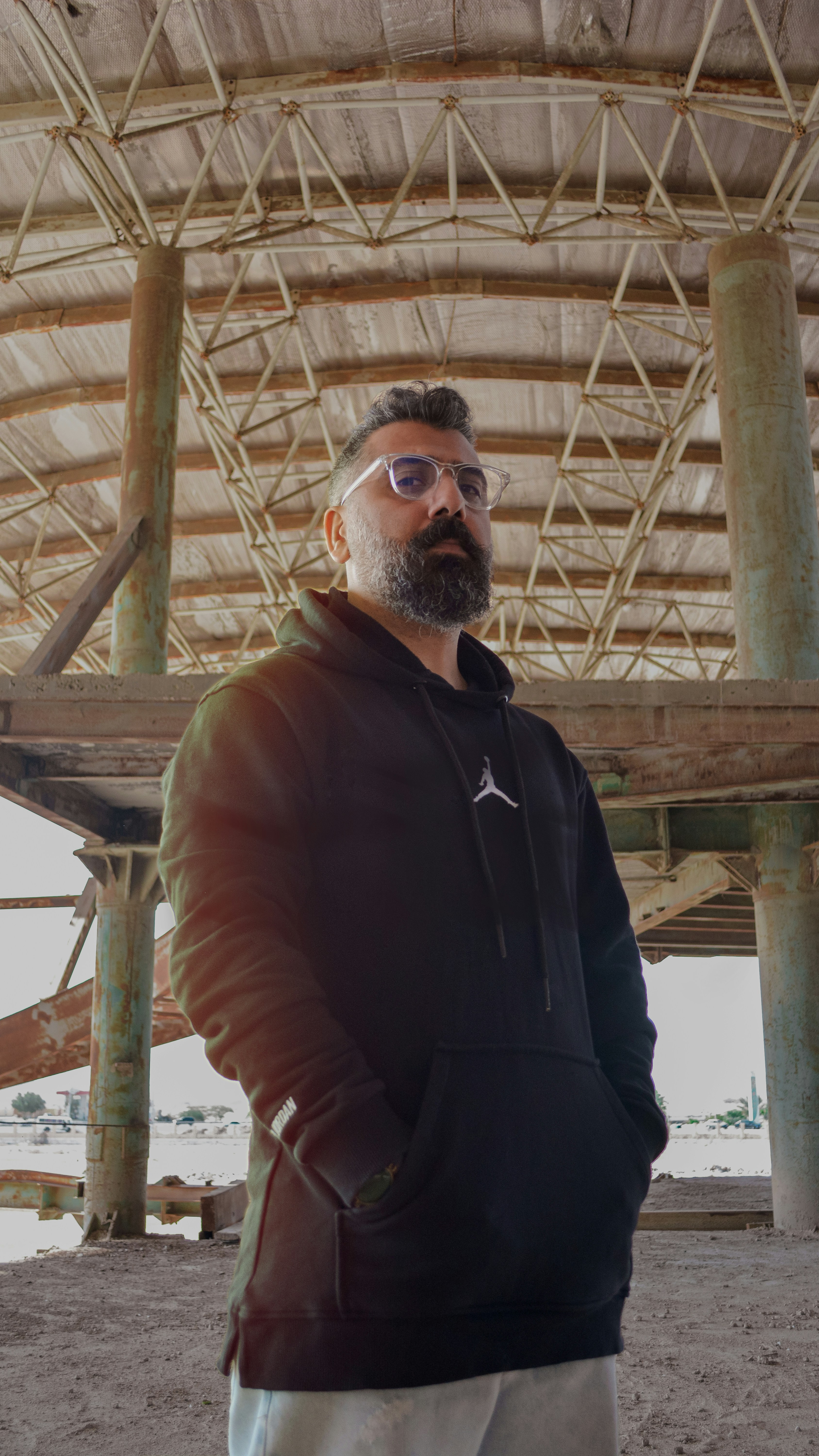 A man standing under a wooden structure in the sand photo – Free ...