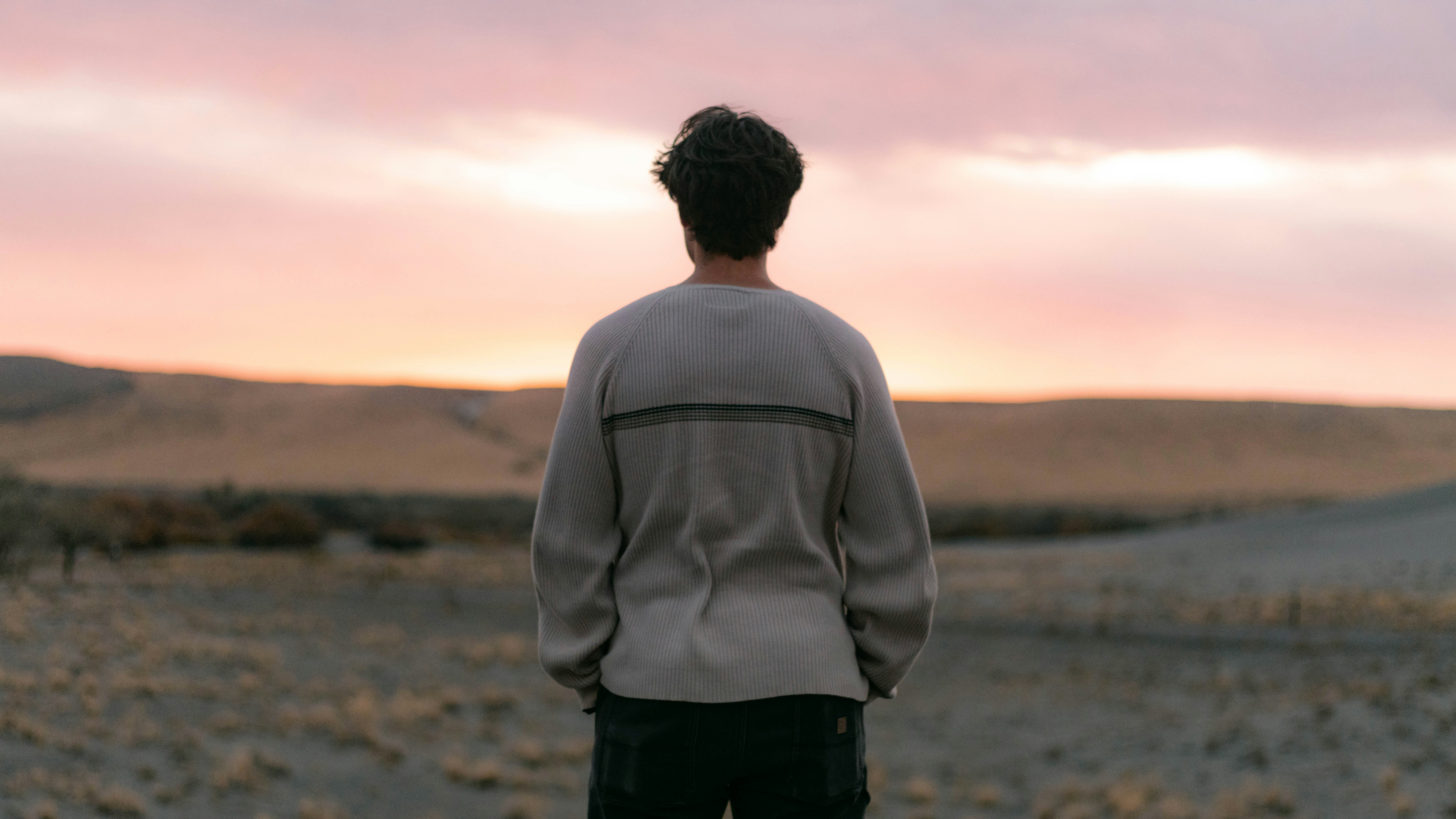 A man standing in a field watching the sun set photo – Free Desert ...