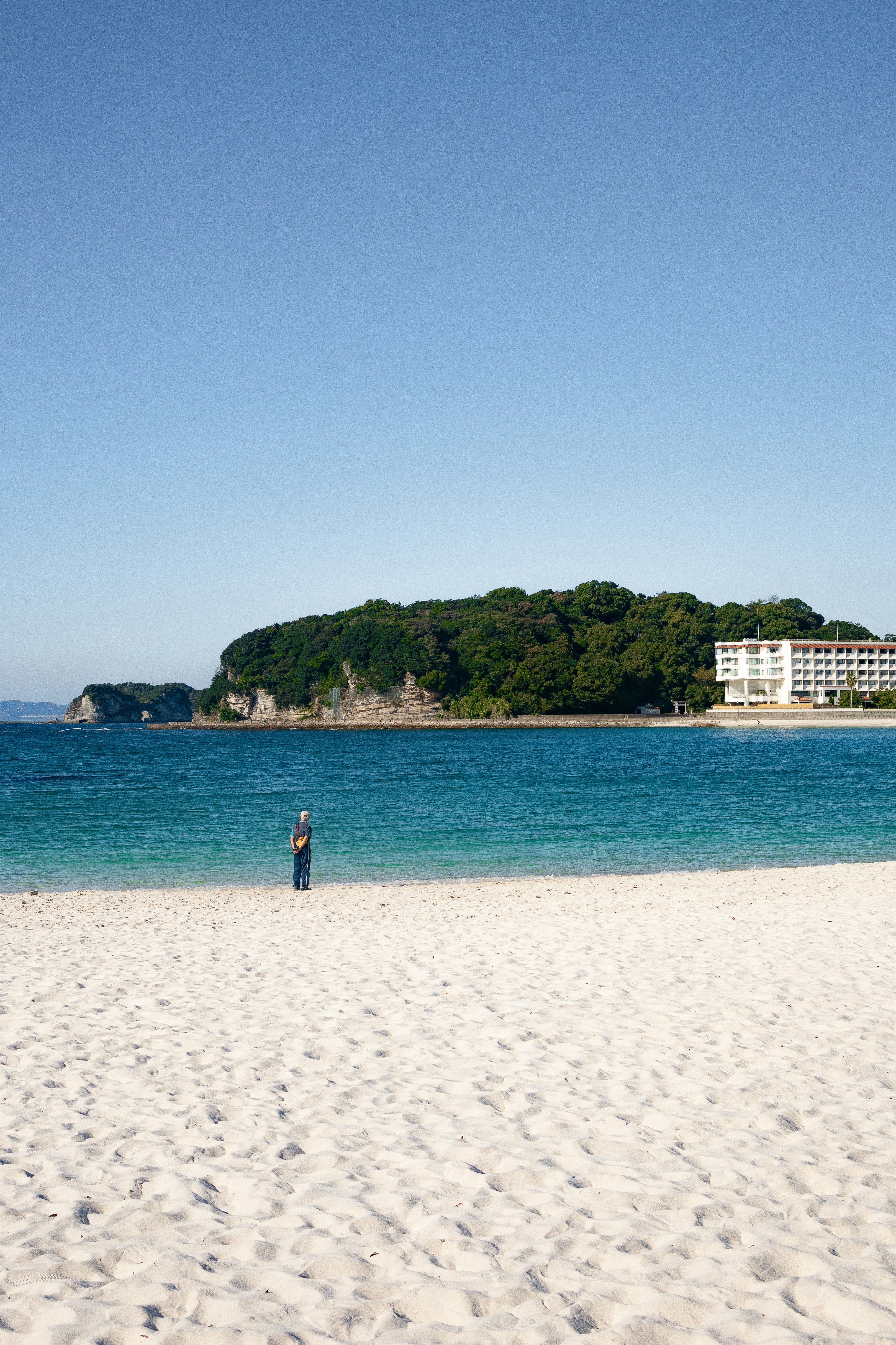 Lone Figure at the Coastal Edge: Sand, Sea, and Green Promontory