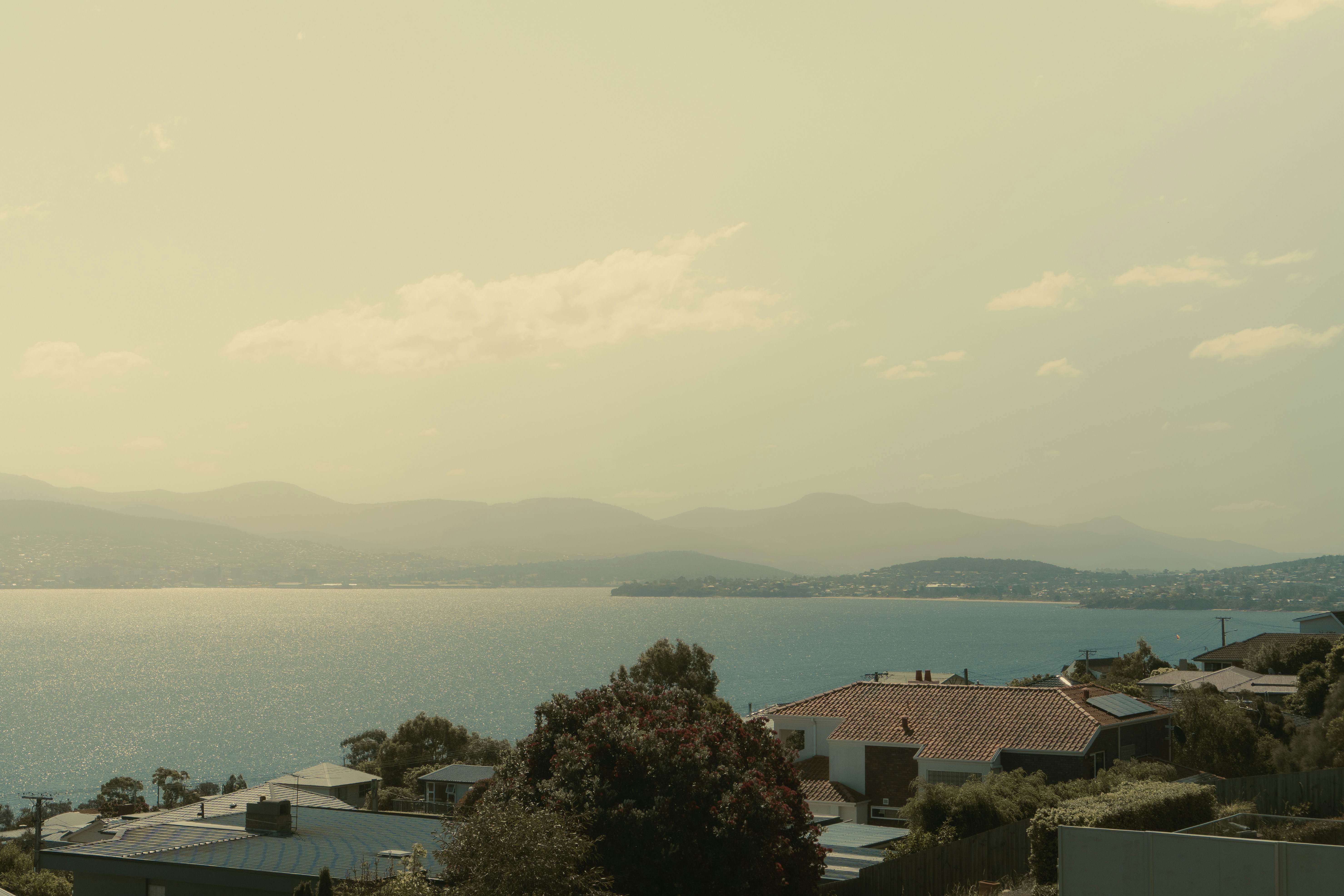 Expansive view of a tranquil body of water framed by hills under a soft, cloudy sky.