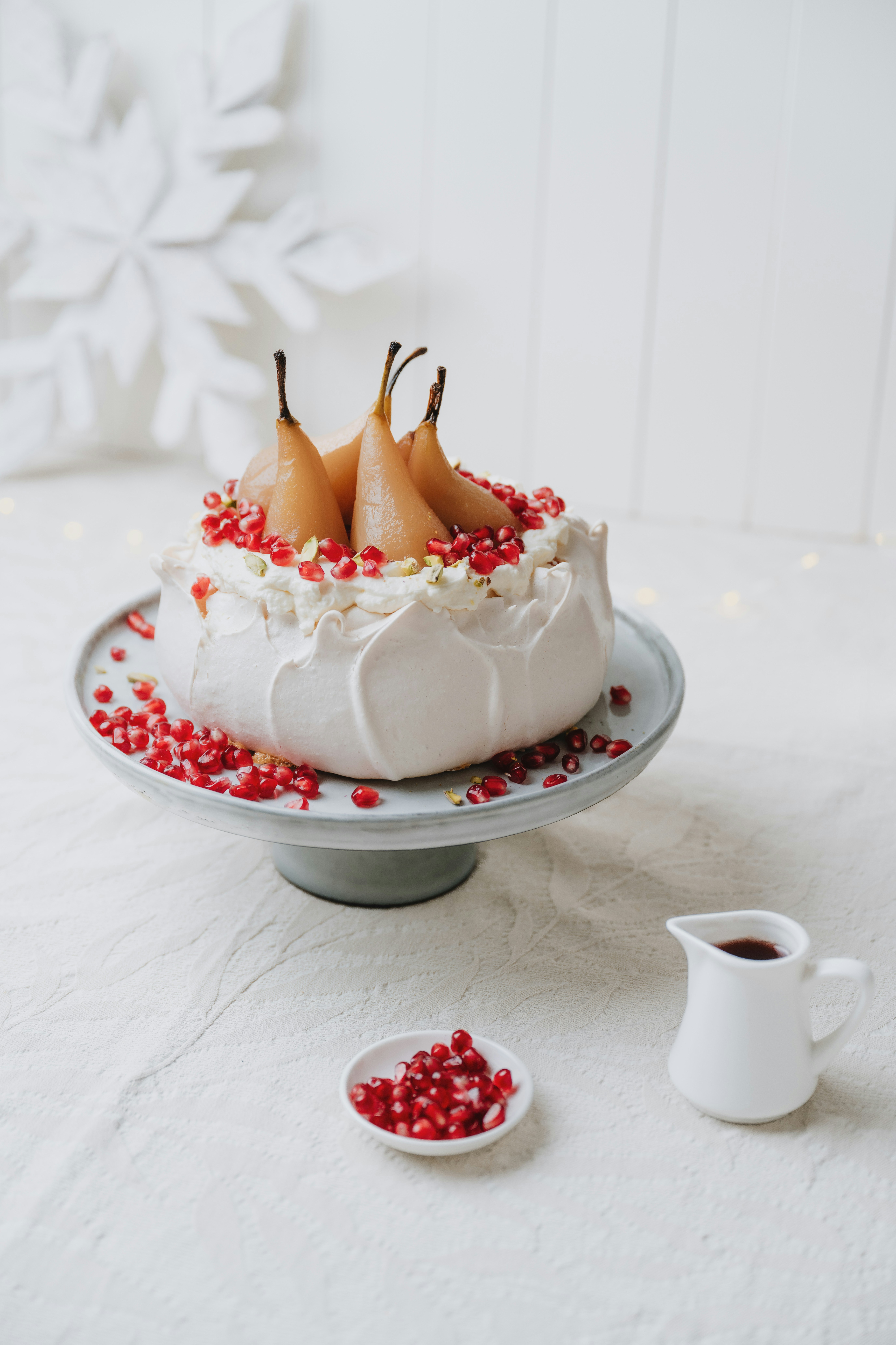 White cake with poached pears and pomegranate seeds on a cake stand, set against a white background with soft lighting.