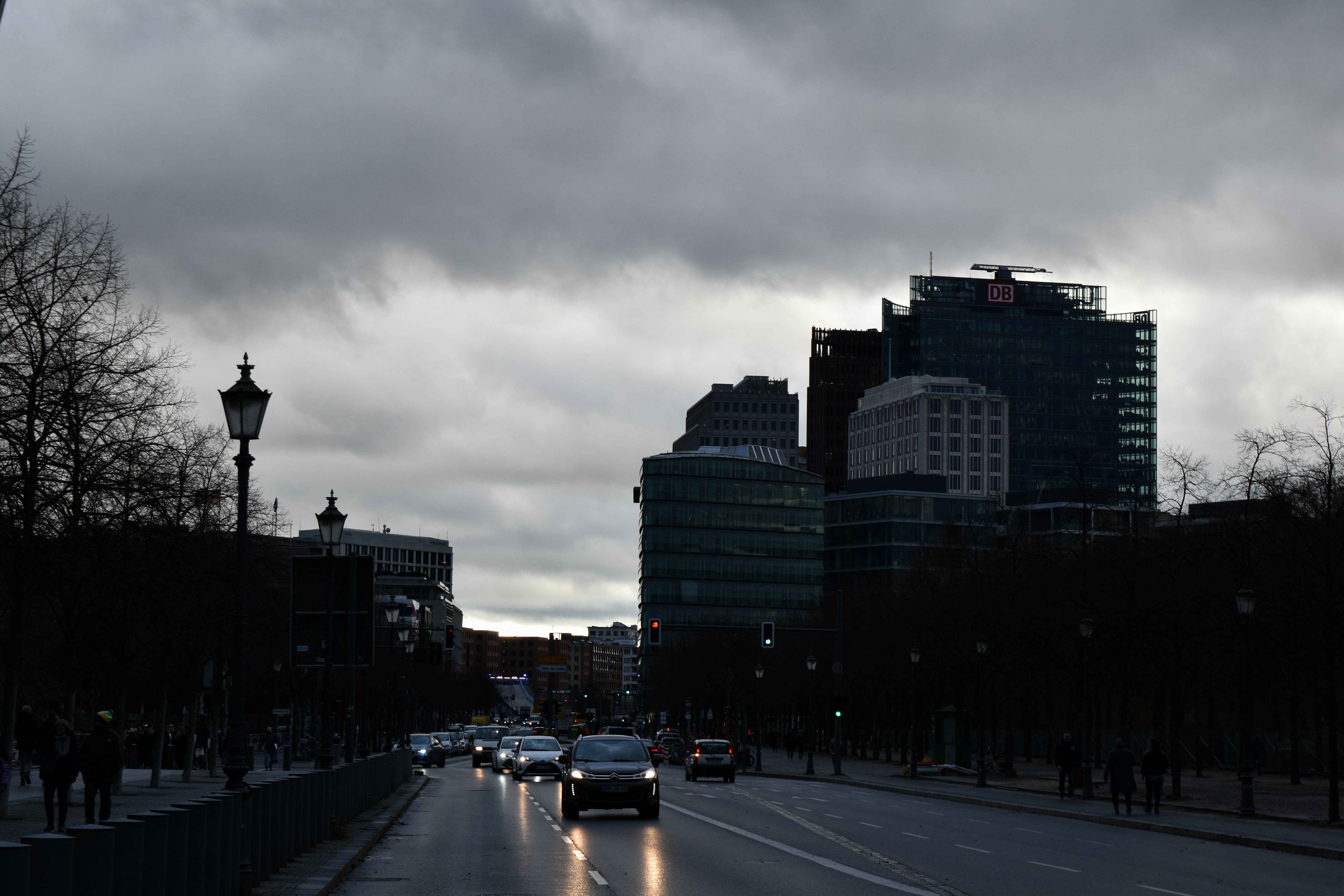 City street bustling with vehicles under a dramatic, overcast sky, showcasing modern architecture and a sense of motion.
