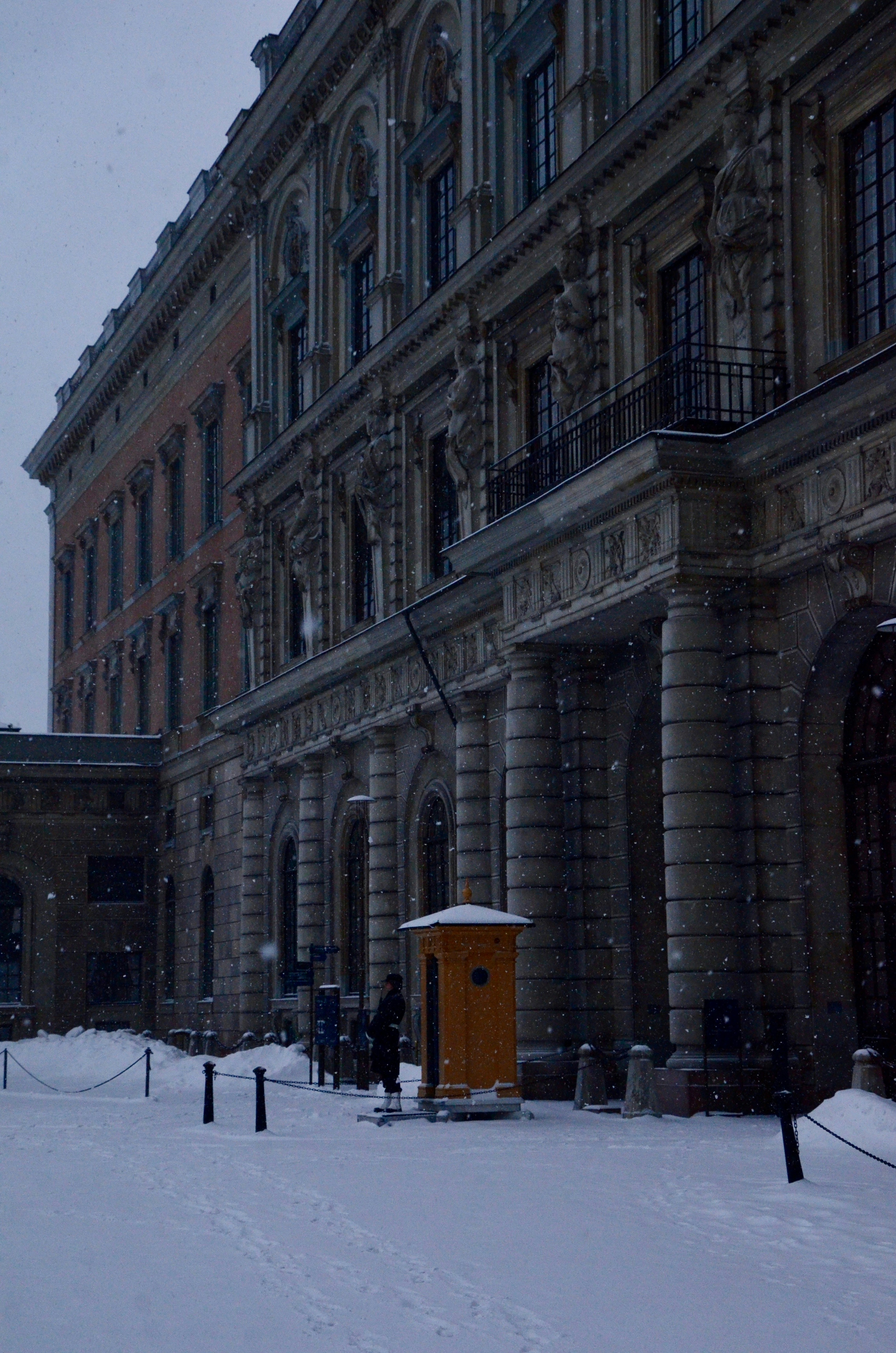 Snow gently falls around the grand architecture of a historic palace.